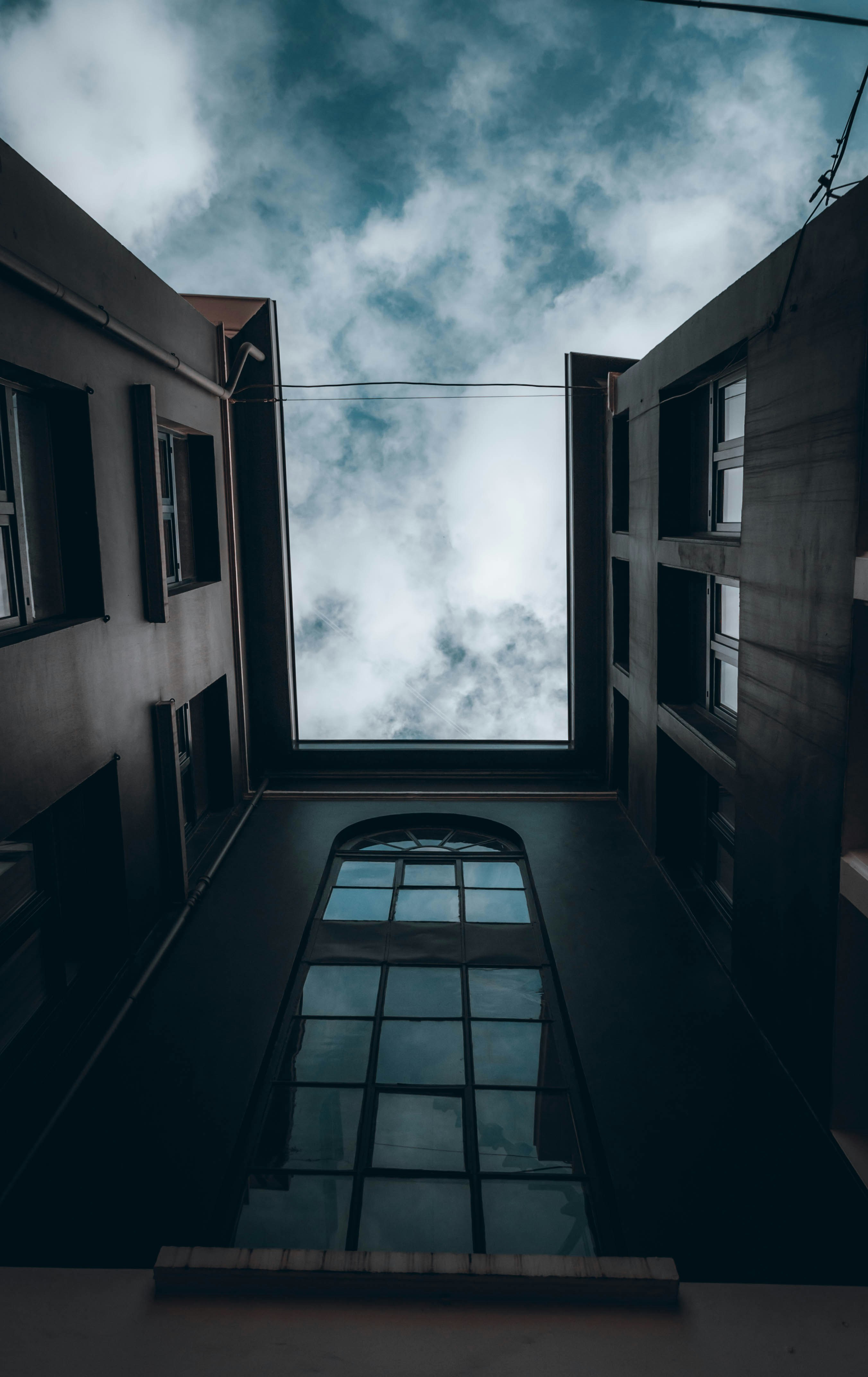 Architectural view from below, showcasing a large window framed by surrounding buildings against a cloudy sky.