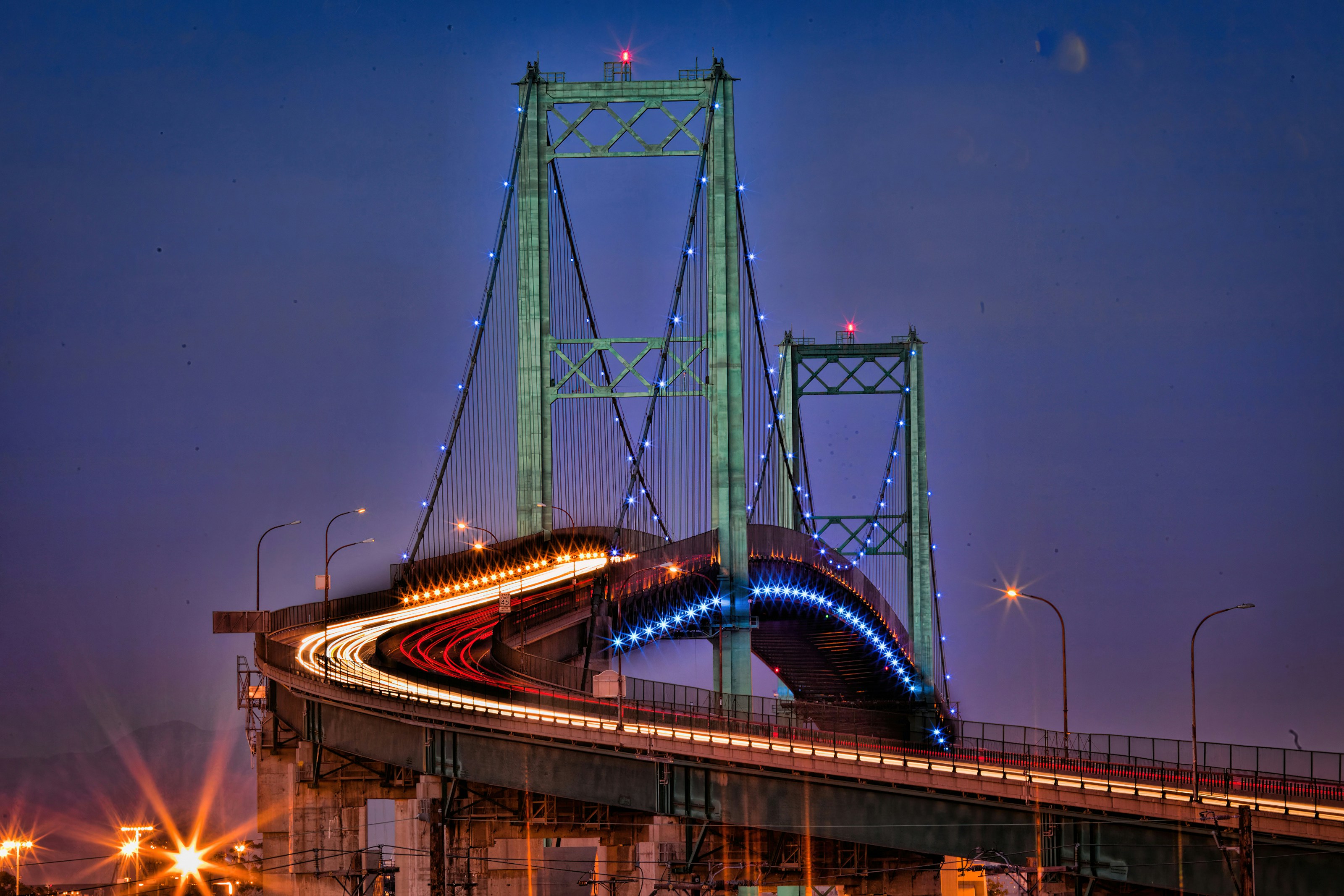 A vibrant bridge adorned with colorful lights, showcasing the dynamic flow of traffic against a twilight sky.