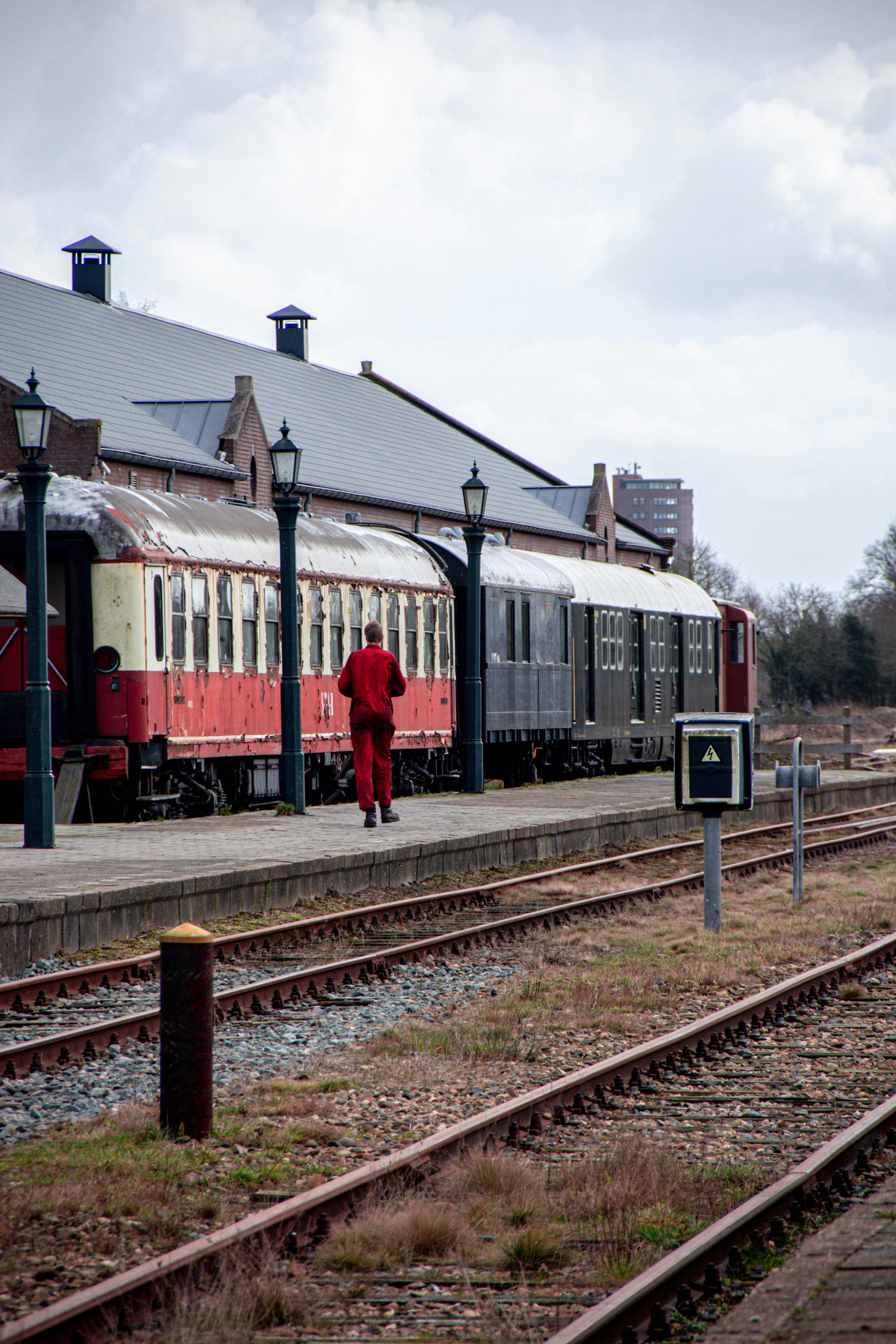 Crimson Figure on the Platform: A Quiet Sentinel beside Vintage Carriages