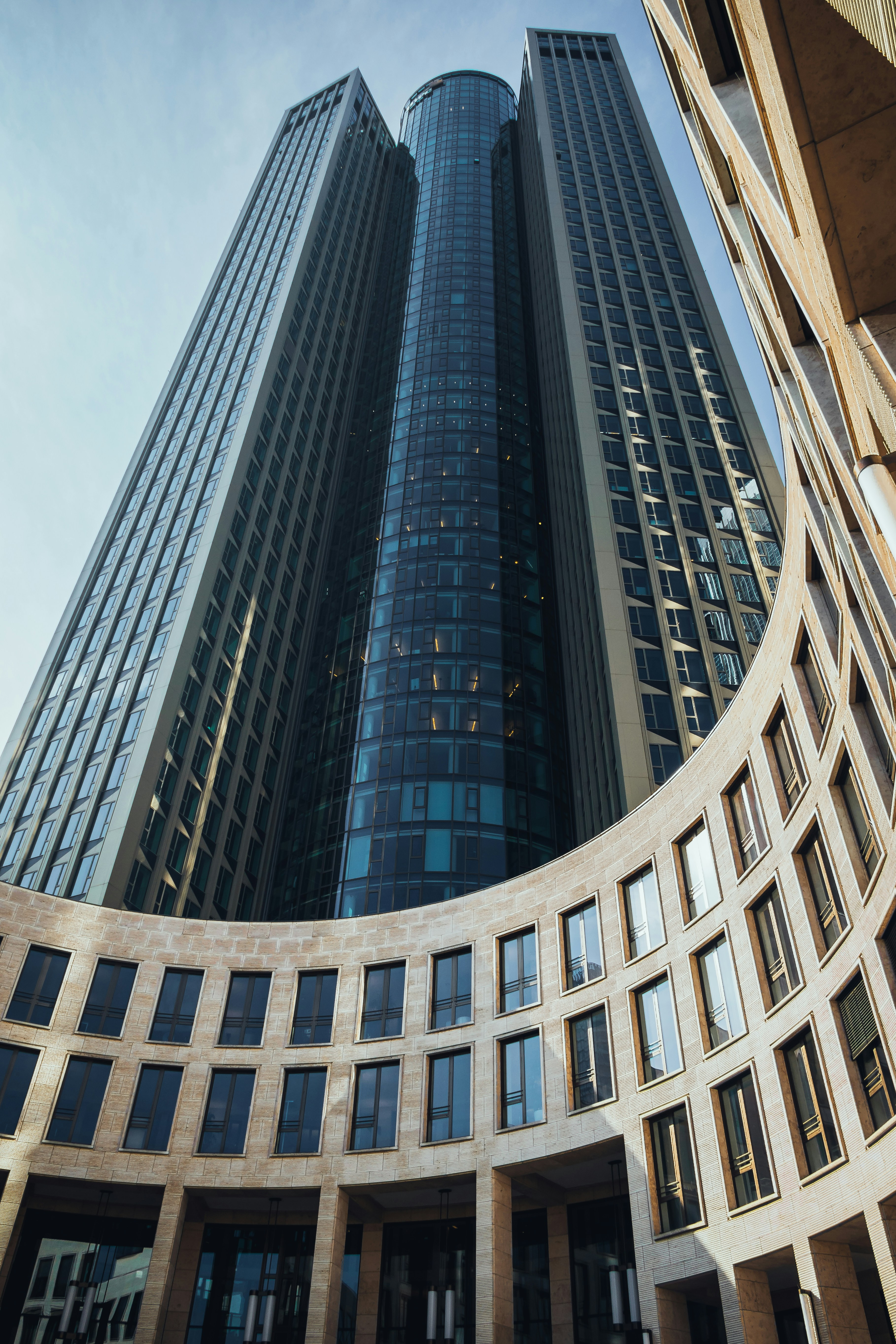 Modern skyscrapers framed by a circular architectural design, showcasing a blend of glass and stone elements. The upward angle emphasizes the towering structures.