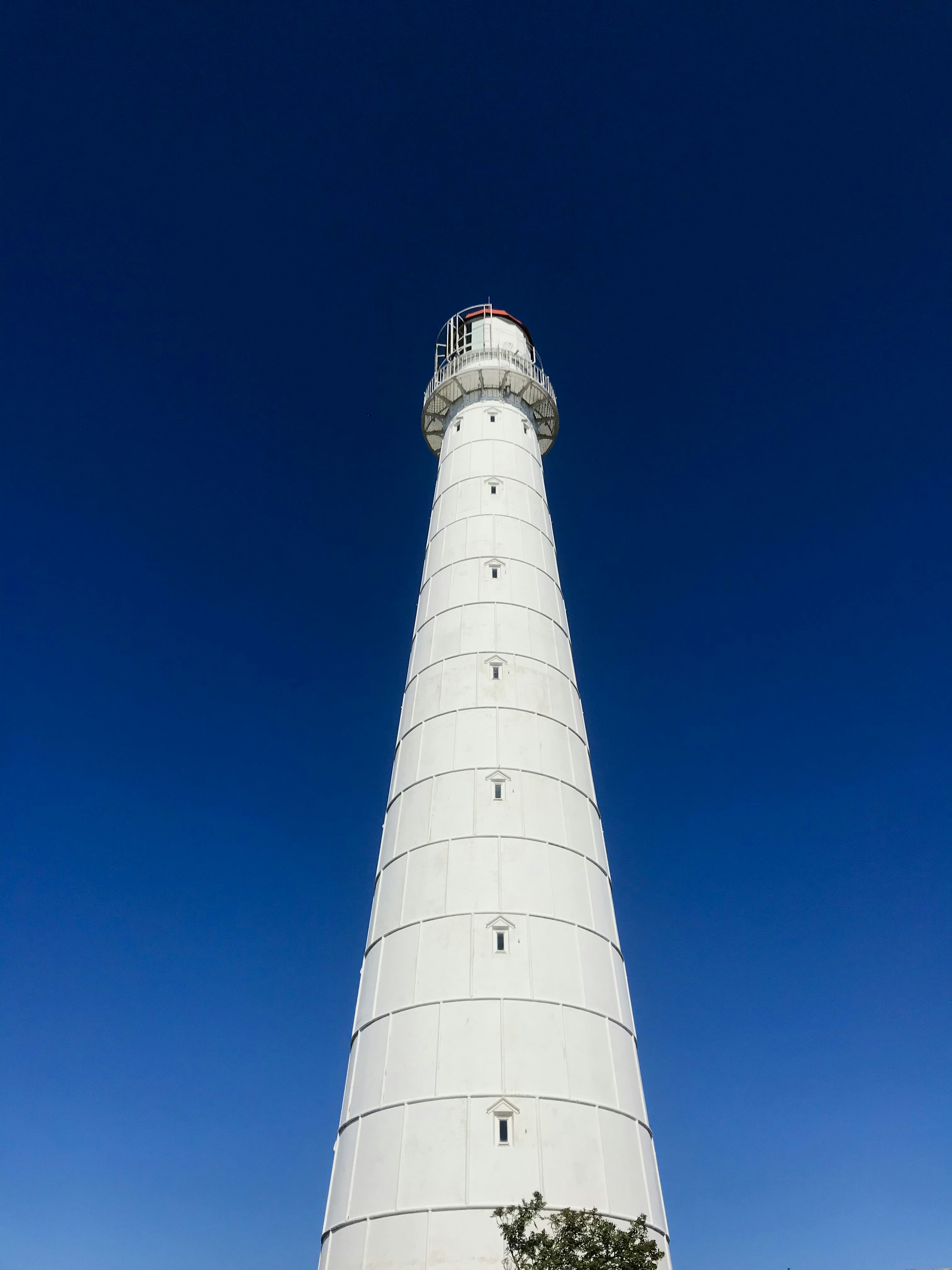 A tall white lighthouse stands against a clear blue sky, symbolizing safety and navigation. The structure showcases intricate architectural details.