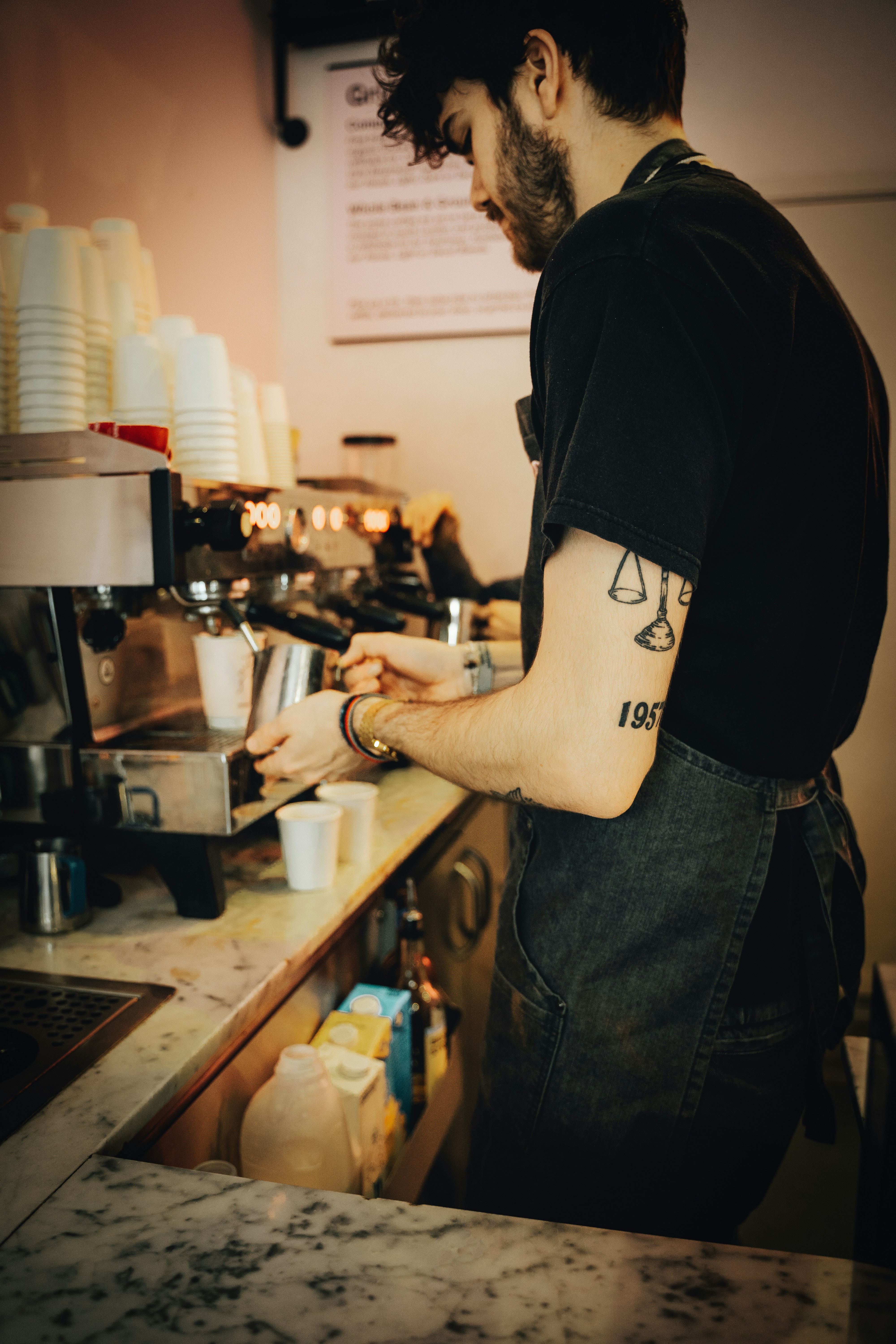 Barista skillfully prepares coffee at a bustling café, showcasing the espresso machine and cups. The focus is on the intricate process of brewing.