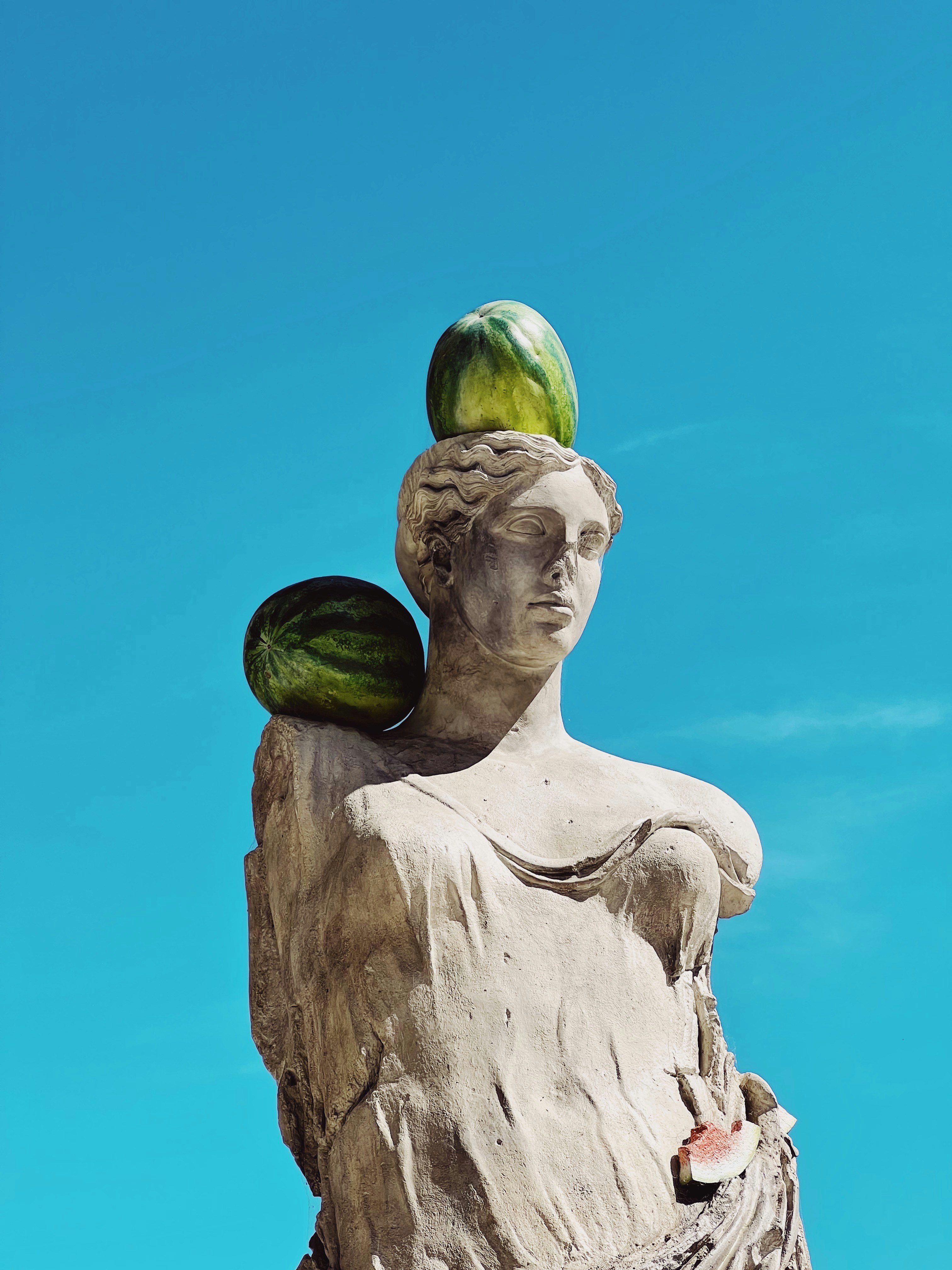 Fruitful Melancholy: A Sculpted Muse with Green Orbs Against a Clear Sky