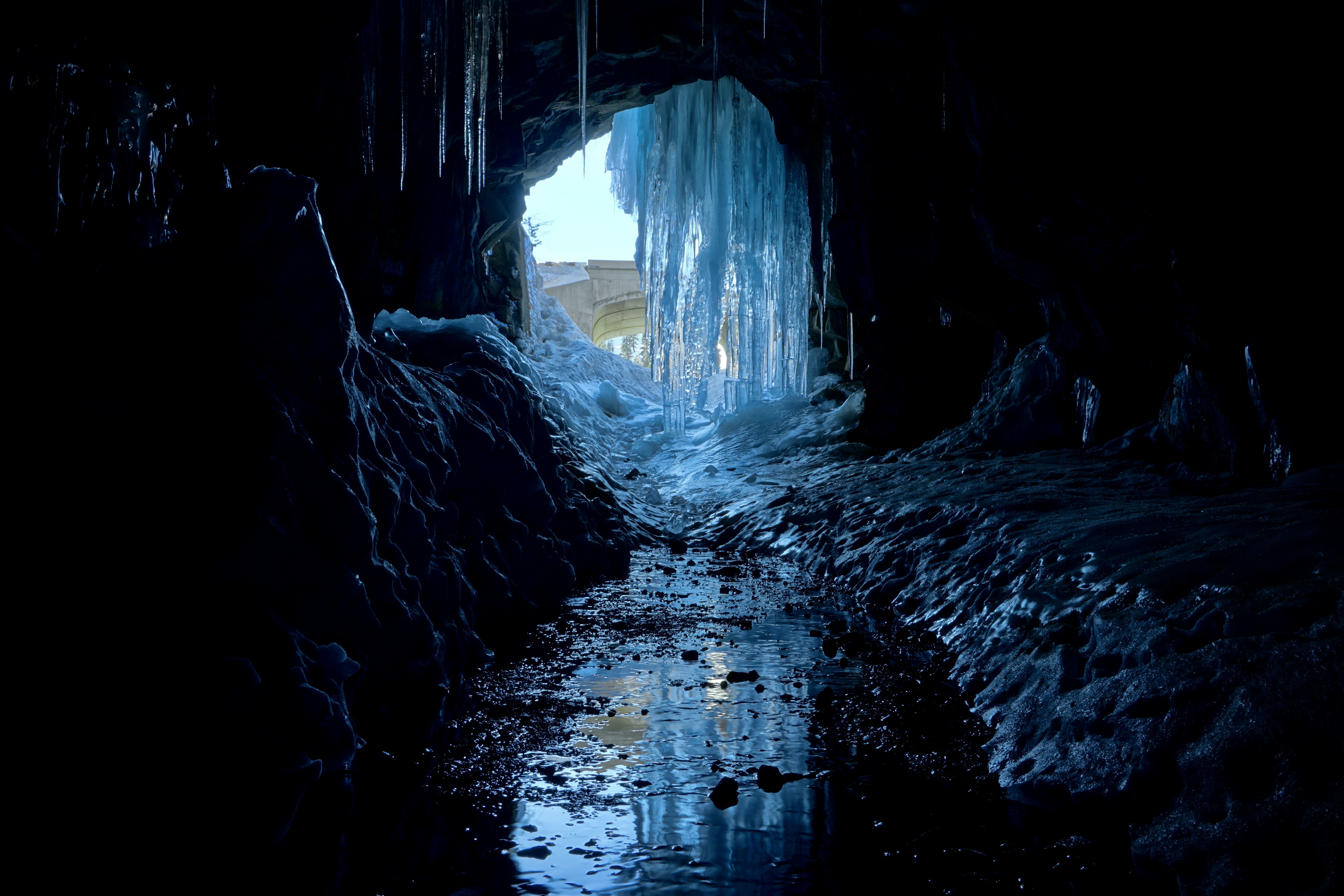 Exit Through the Ice: a Blue-lit Cavern with Icicles and Reflective Pool