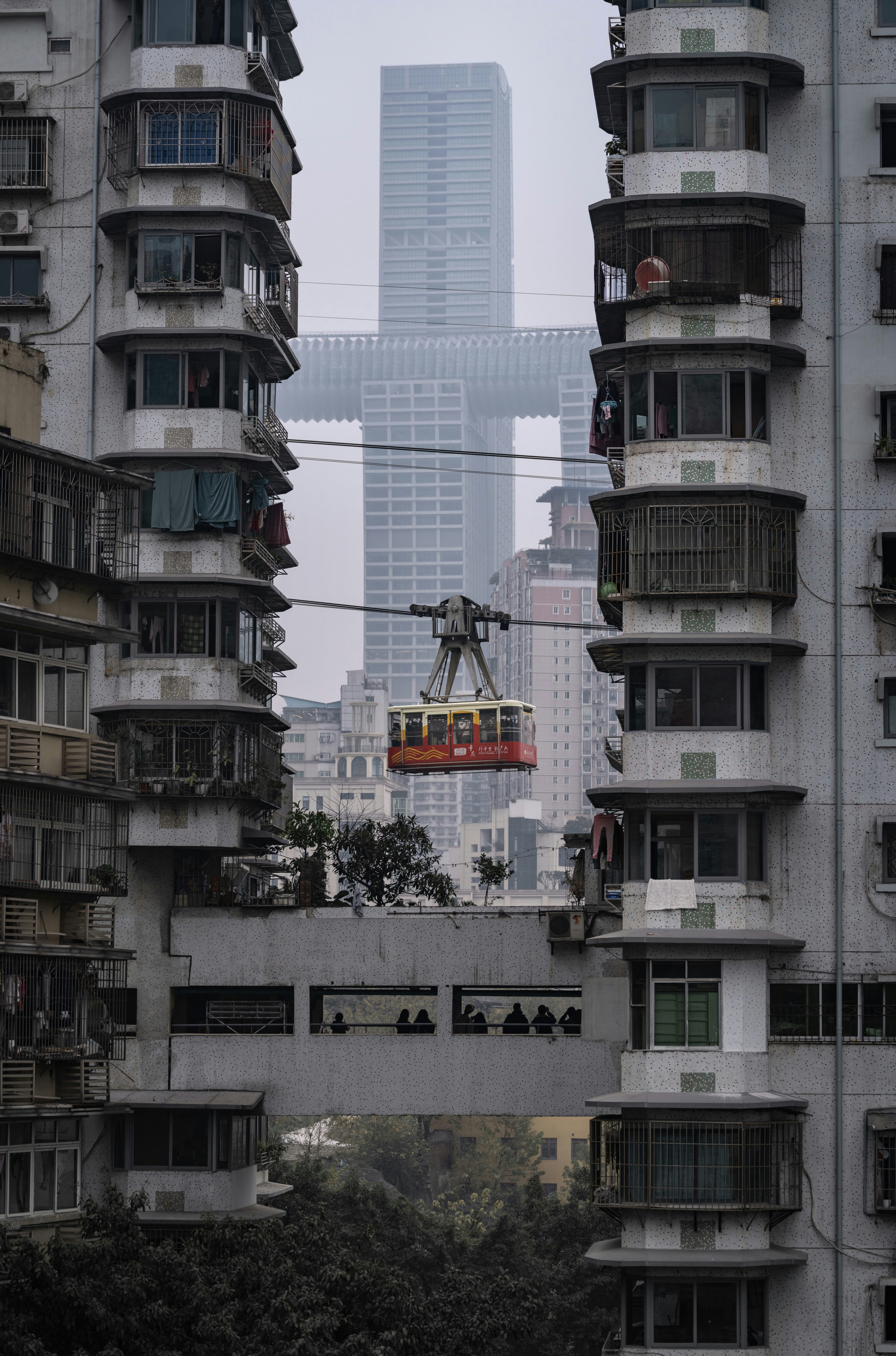 A vibrant cable car traverses between two high-rise buildings, framed by the modern skyline. The contrast of architectural styles highlights urban life.
