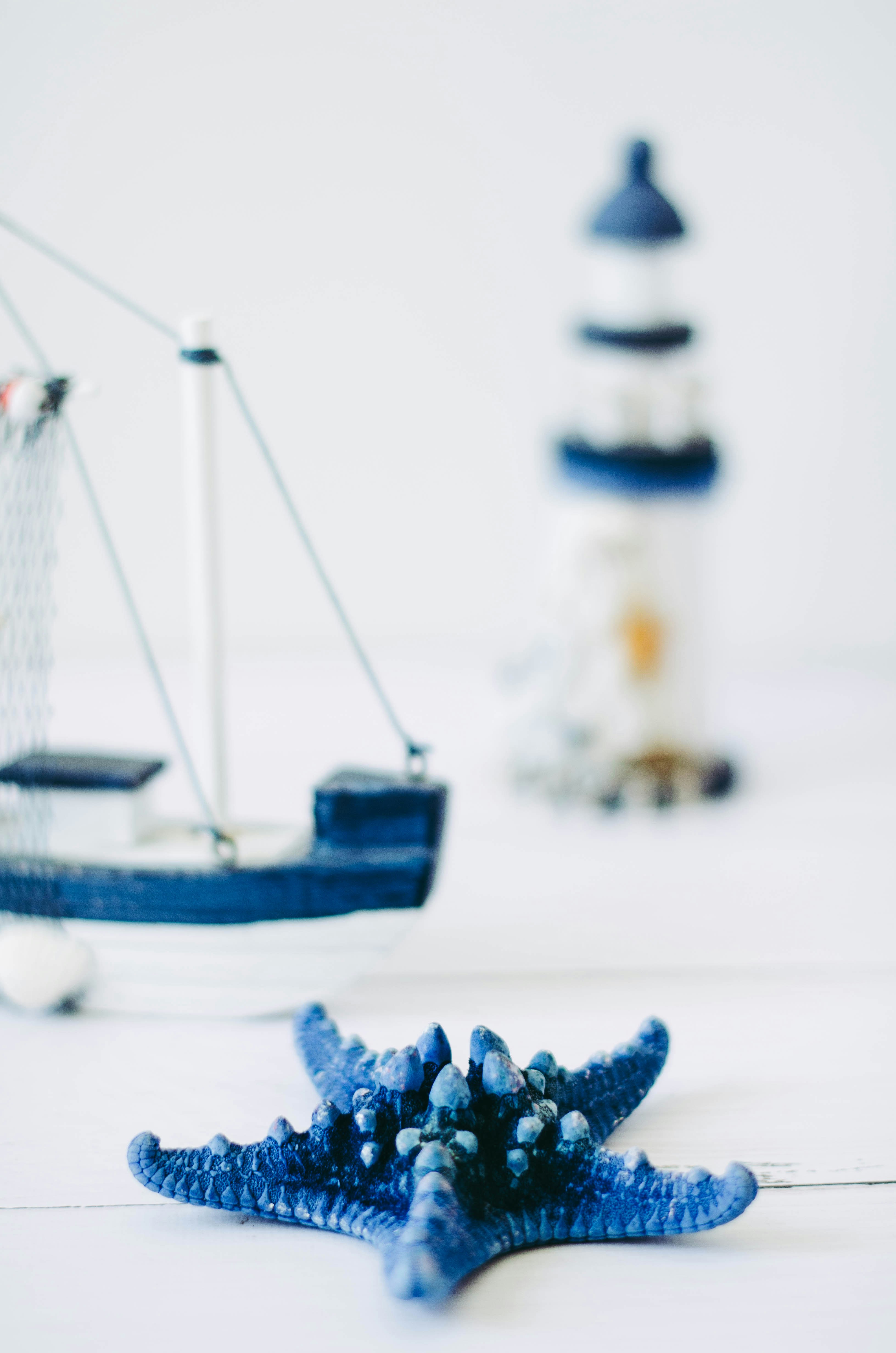 Blue Starfish Foreground: A Maritime Miniature Scene with a Sailboat and a Distant Lighthouse
