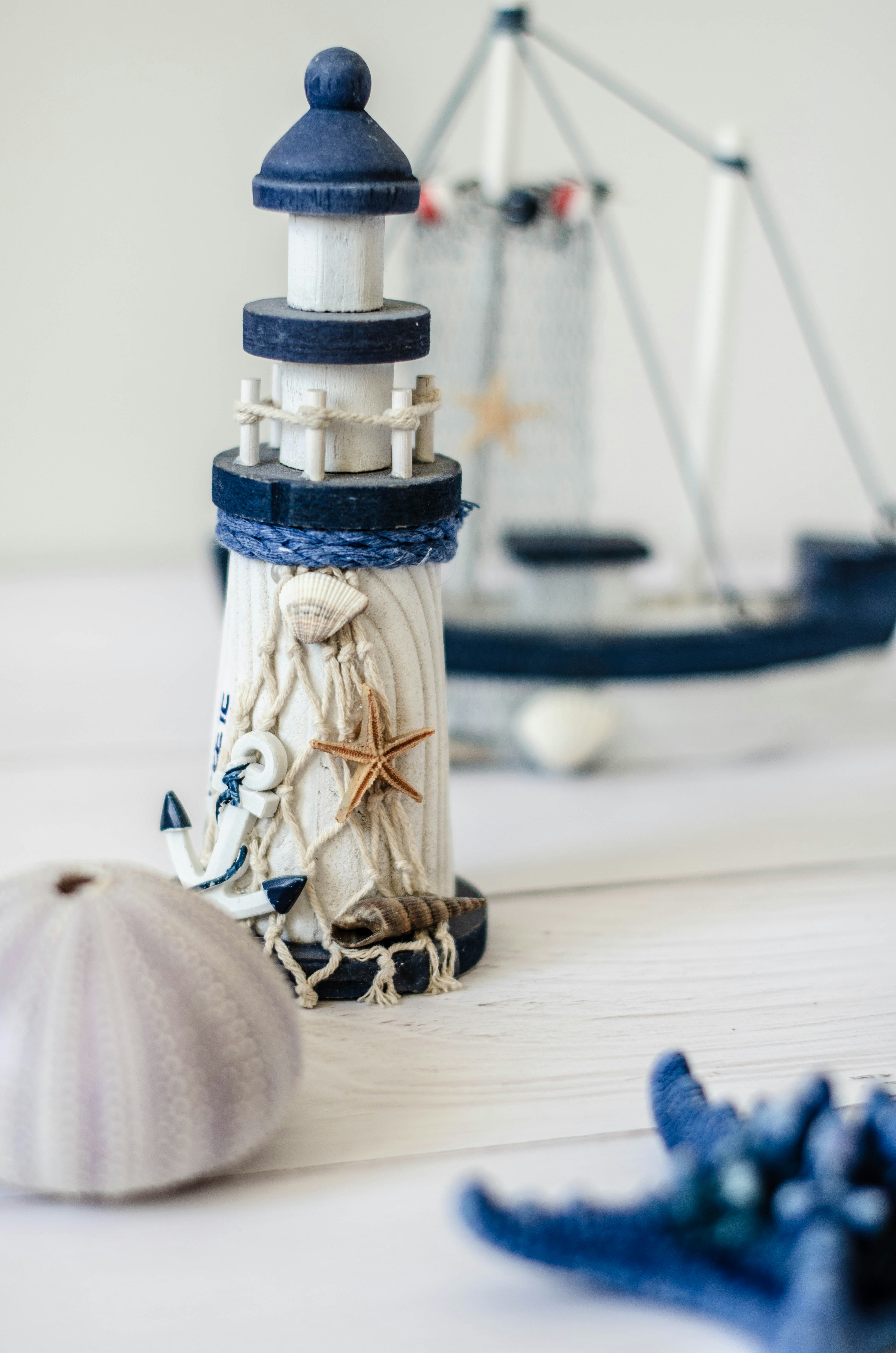 Seaside Sentinel: A Miniature Lighthouse Guards Seashells on a White-Washed Table