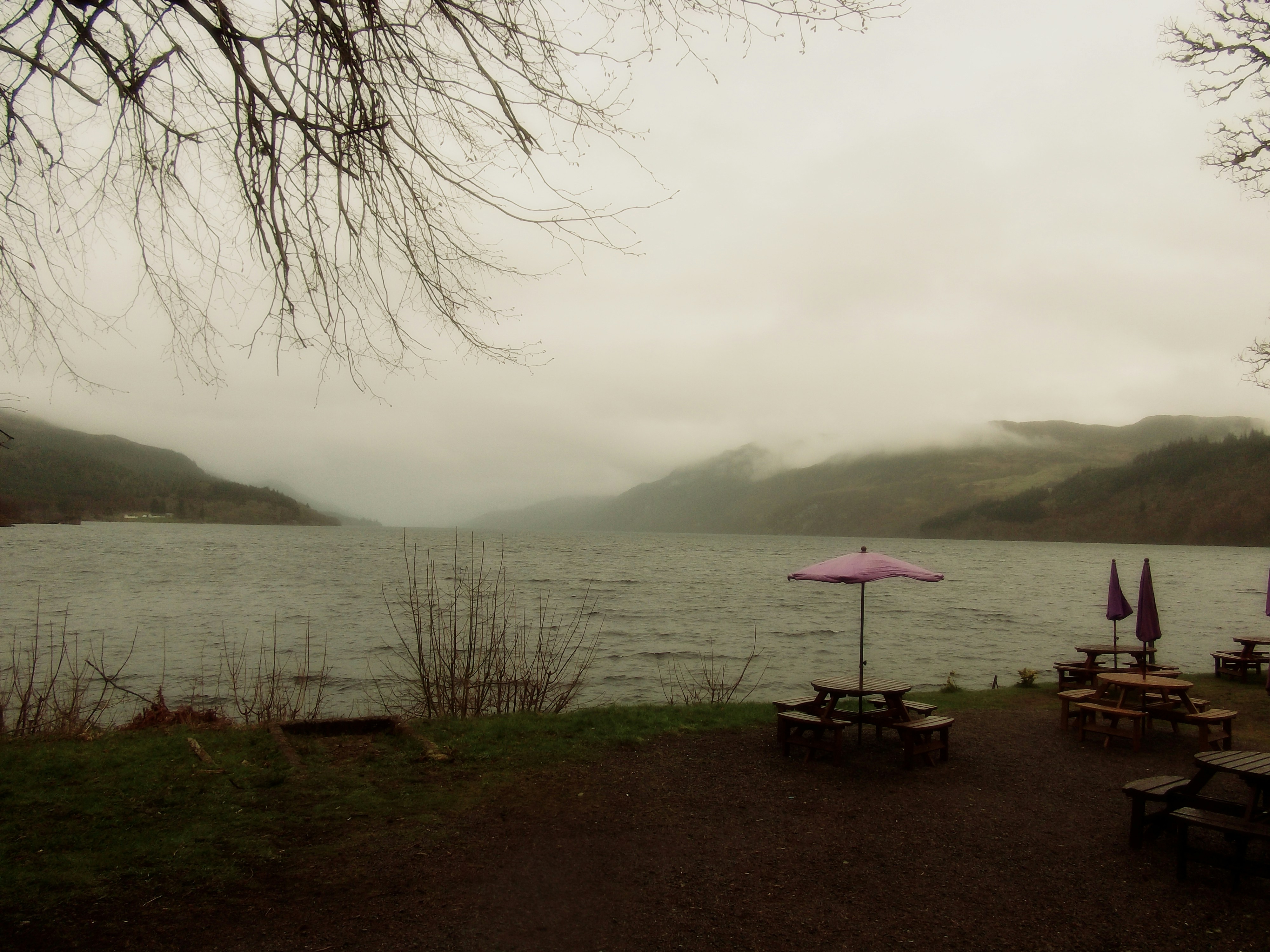 A lake with picnic tables and umbrellas in the rain photo – Free Loch ...