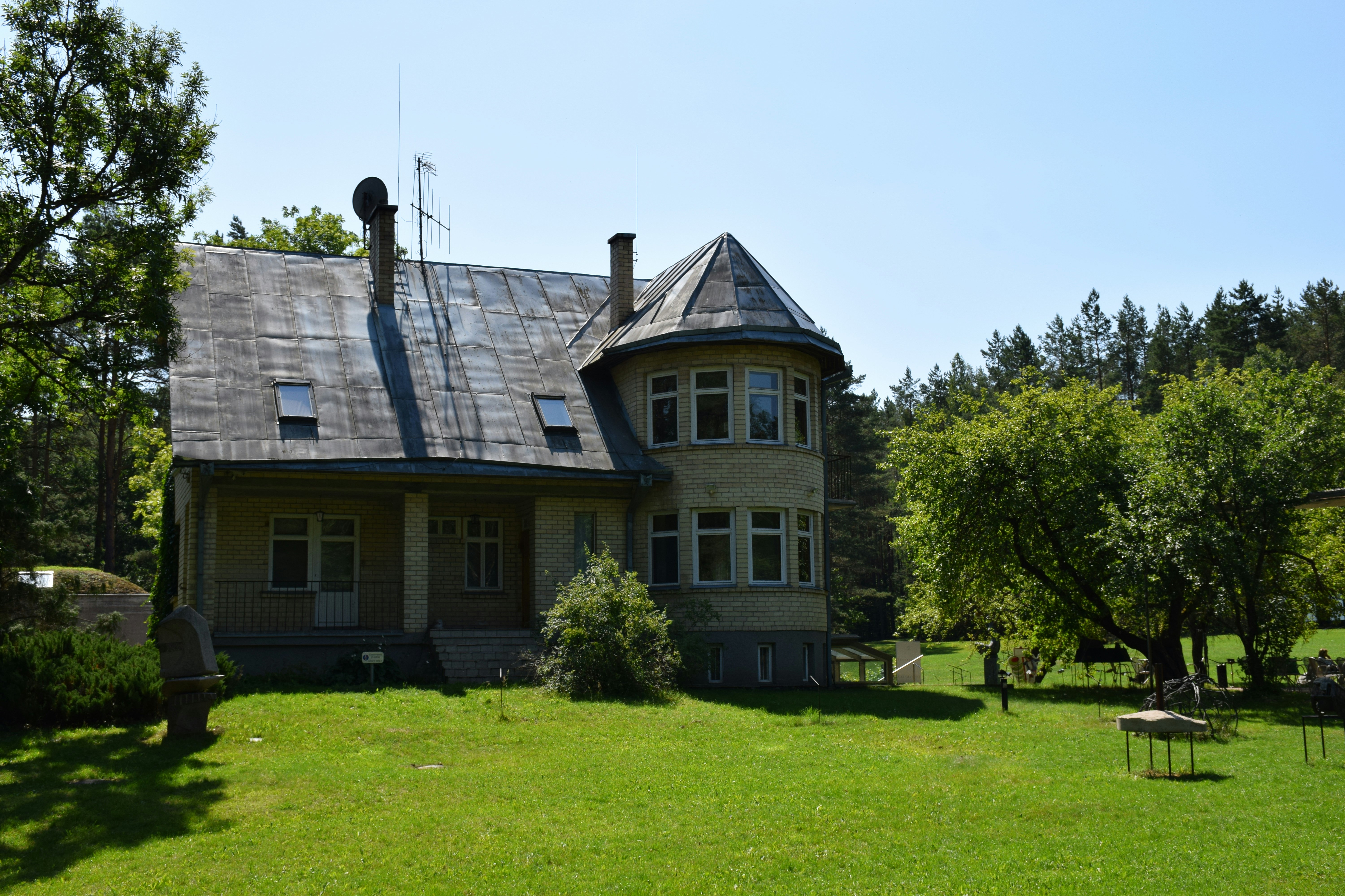 Historic house with a distinctive round tower set in a lush green landscape, surrounded by trees. The building showcases classic architectural elements.