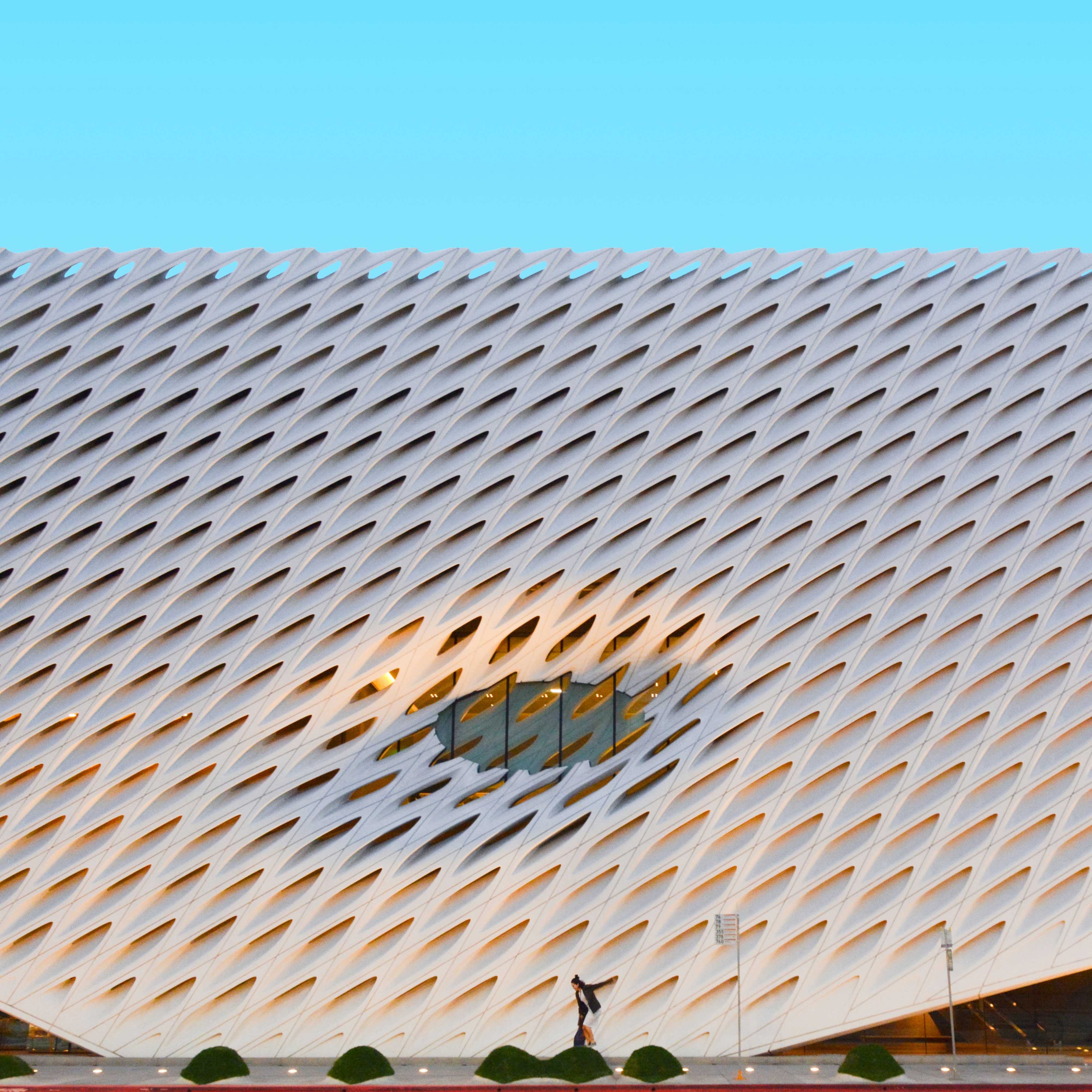 Modern architectural facade featuring a dynamic lattice design with a prominent window, set against a clear blue sky.