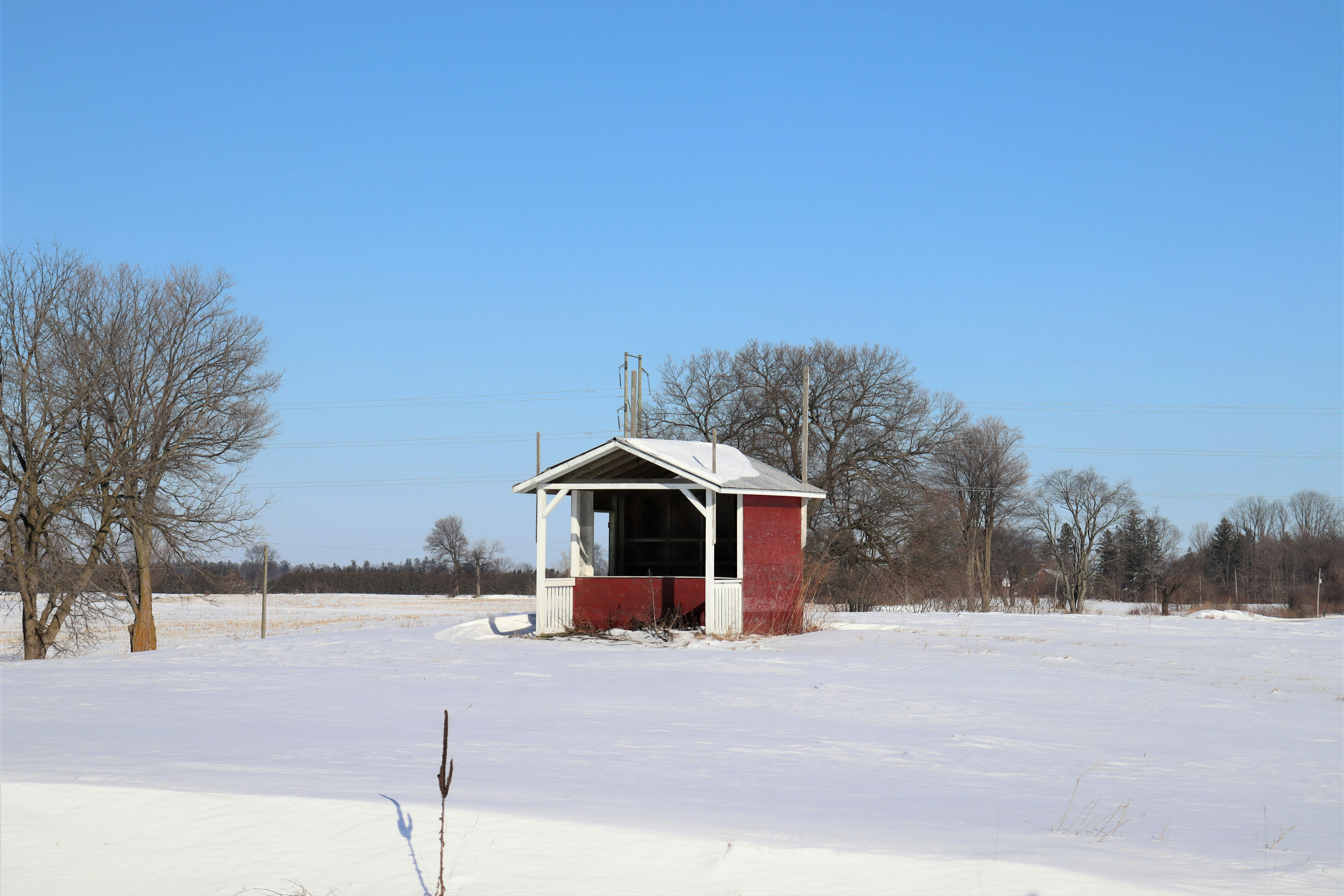 Abandoned red structure surrounded by a vast expanse of snow under a clear blue sky.