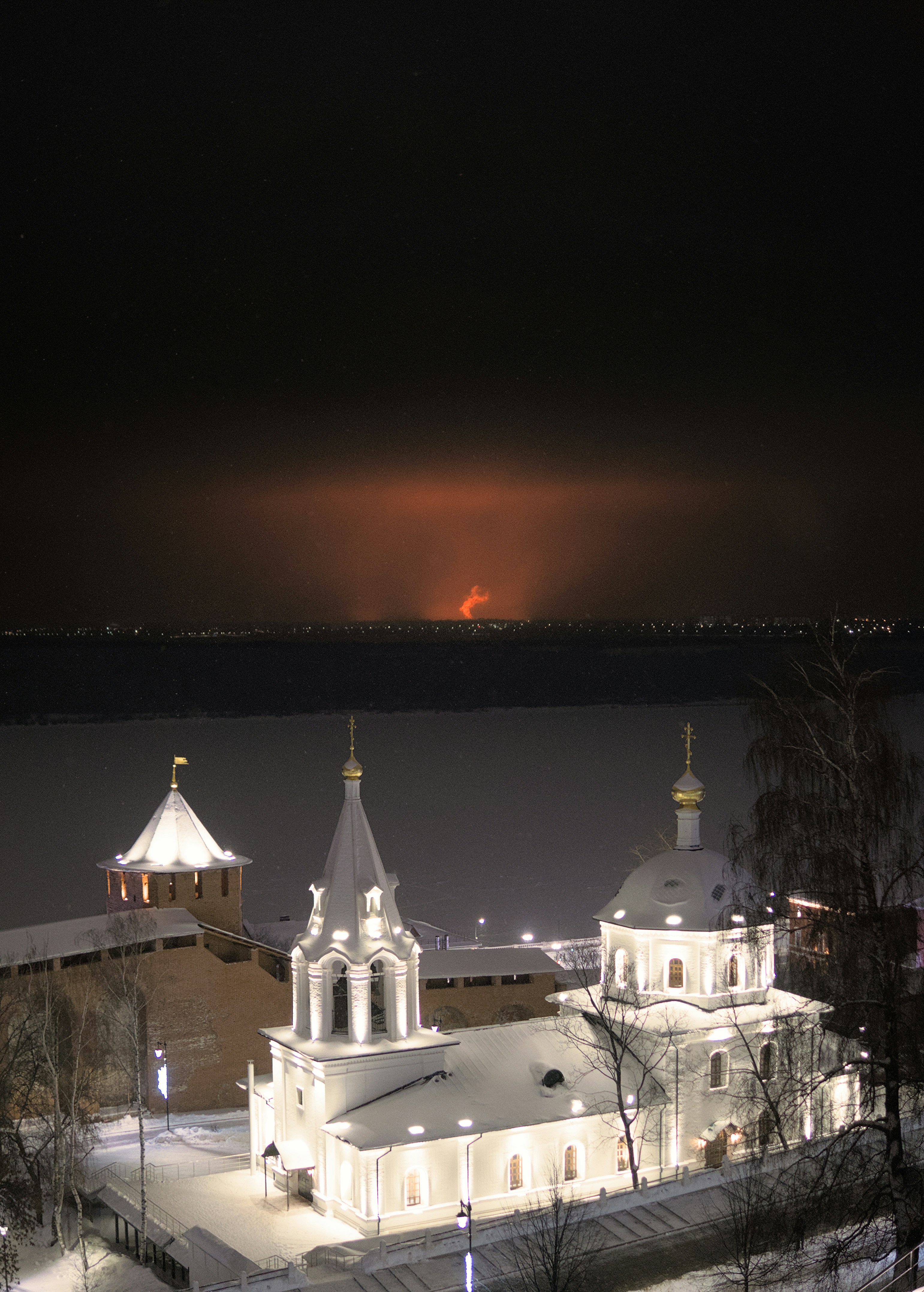 Historic churches and fortifications blanketed in snow, illuminated against a dark sky with distant glowing horizon.