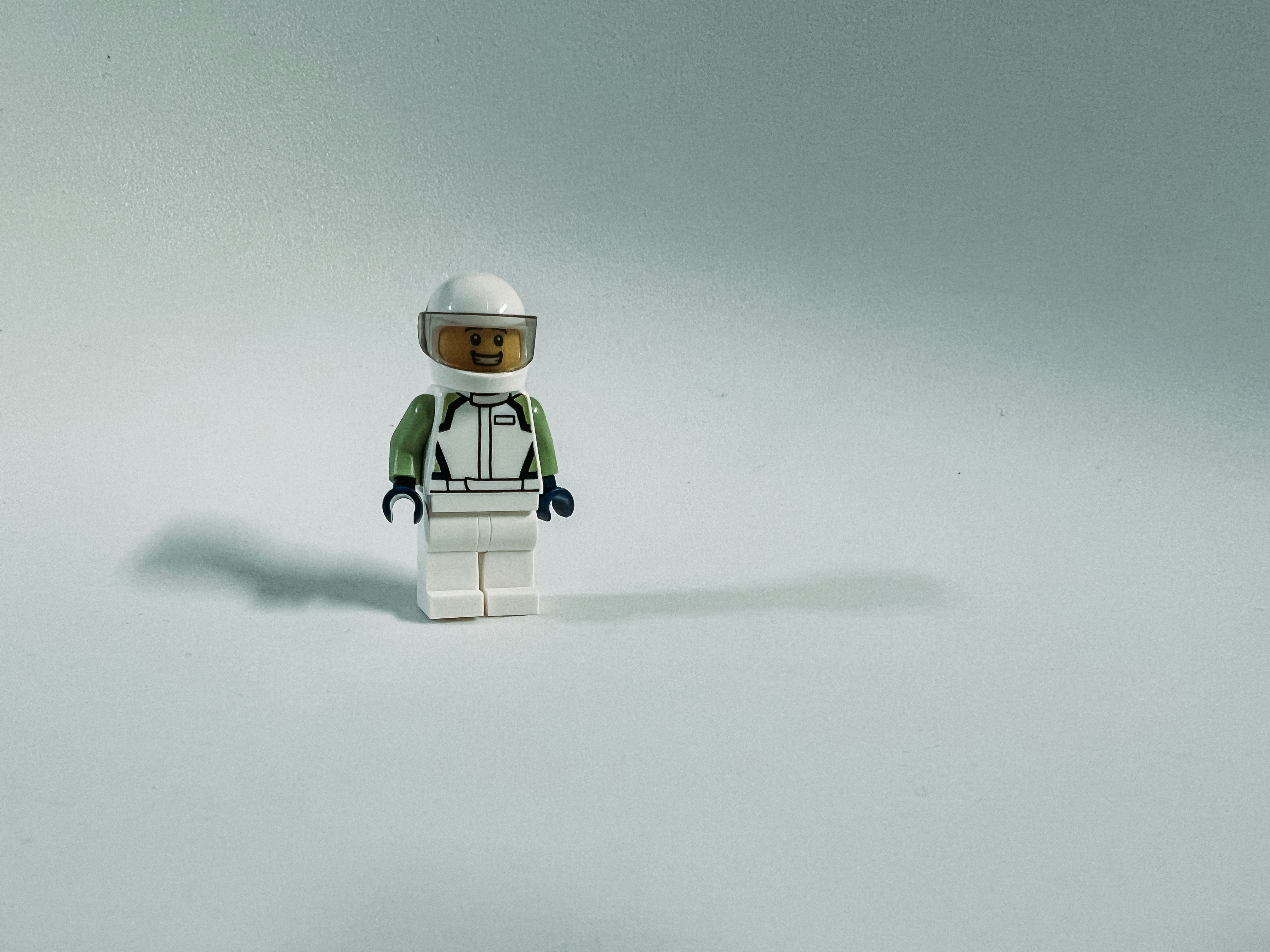 A Lego astronaut figure stands on a smooth surface, casting a gentle shadow against a minimalist backdrop.