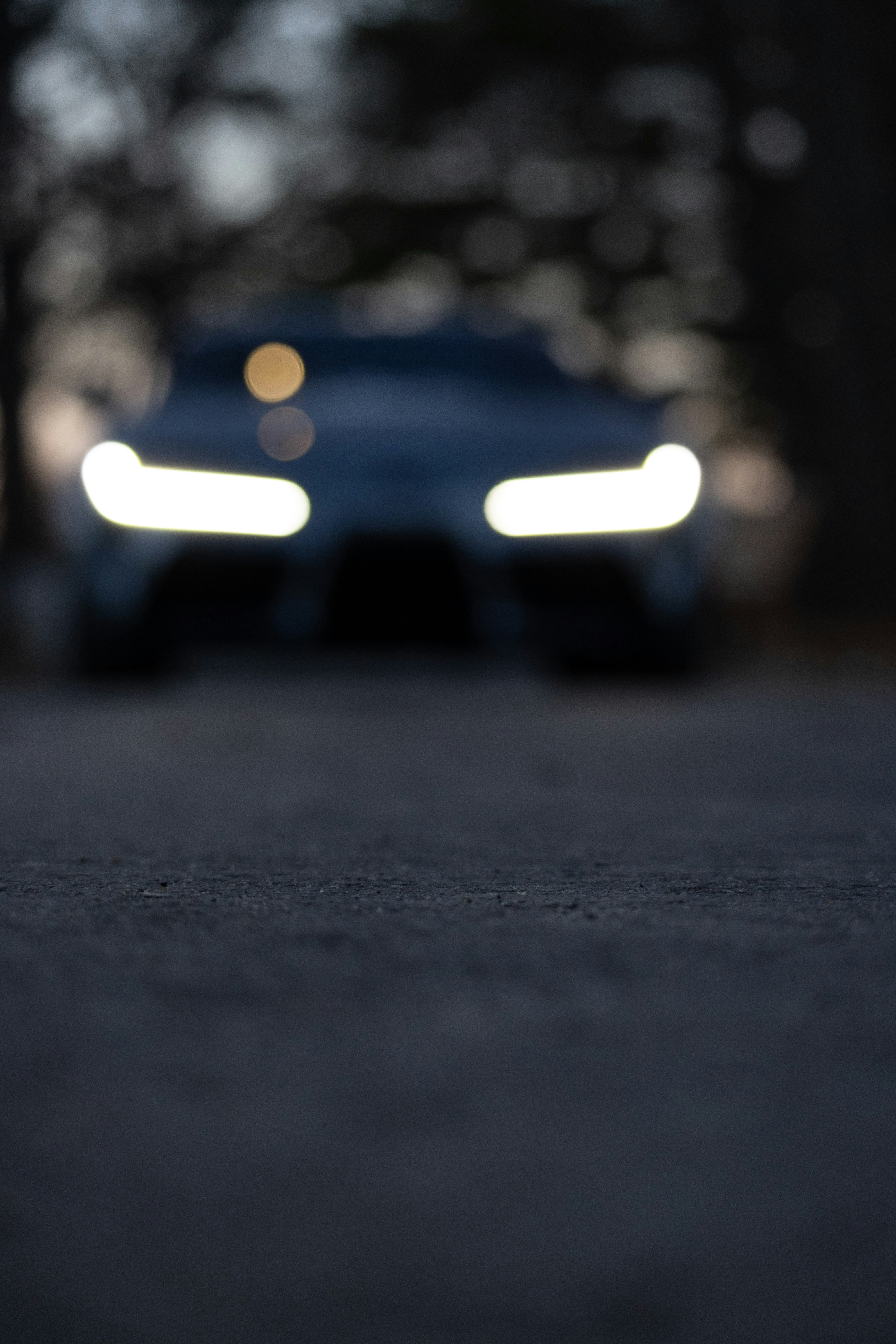A sleek sports car emerges from the shadows, its headlights piercing the dusk, creating a striking contrast against a blurred background.