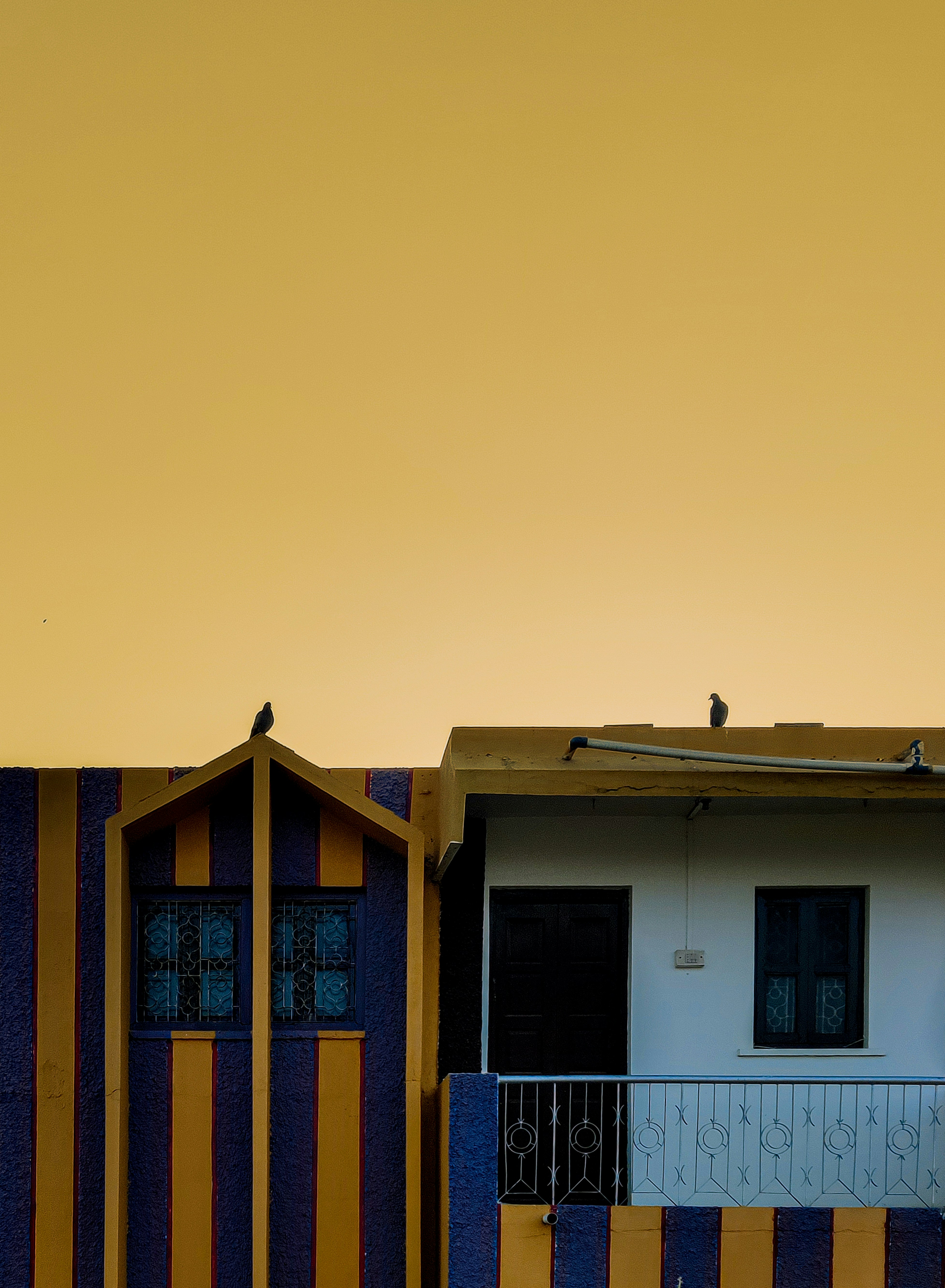 Vibrant building with geometric patterns and two birds perched on the roof against a golden sky.