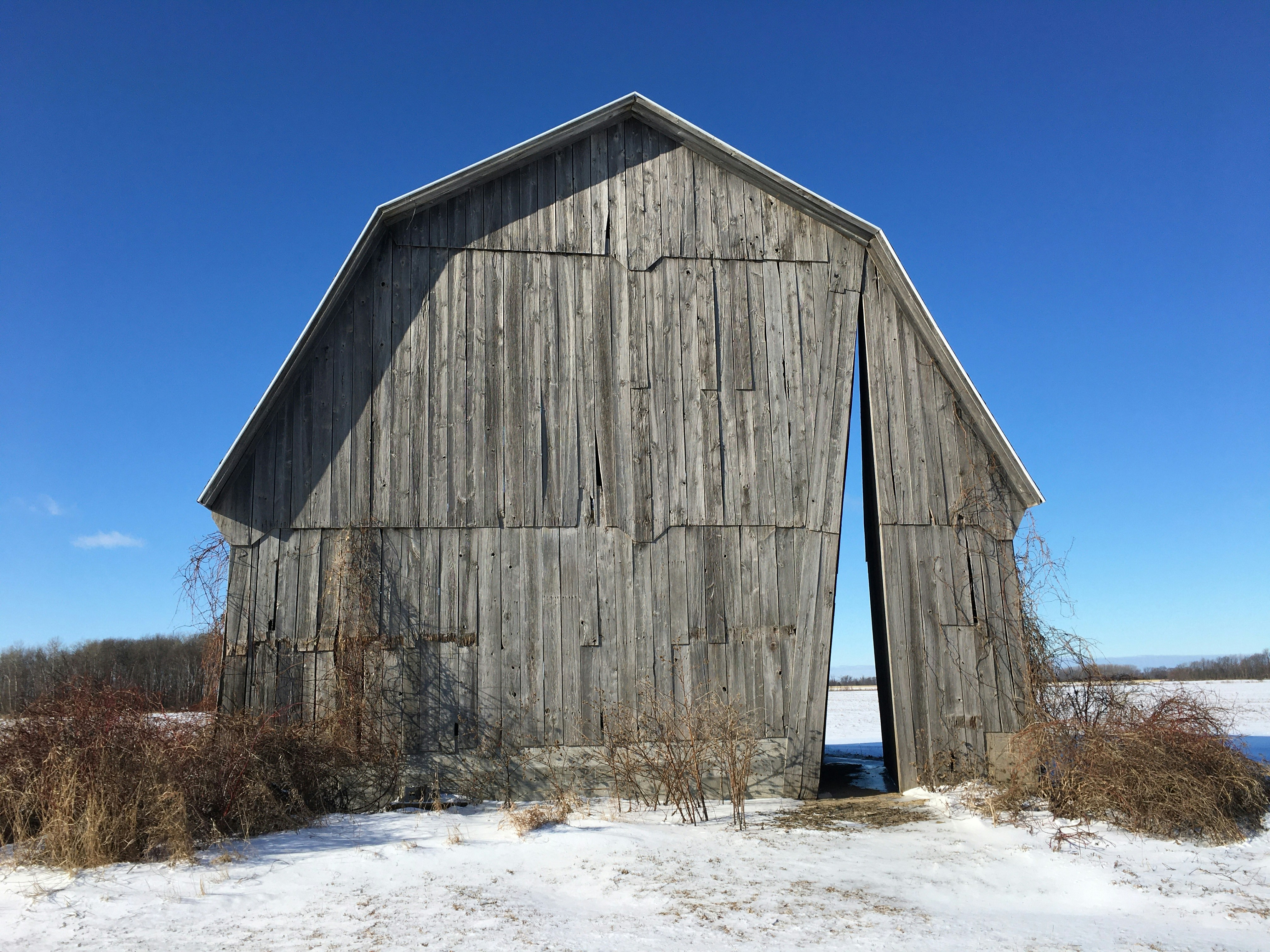 Weathered Barn Amid Snowy Field Under Clear Blue Sky