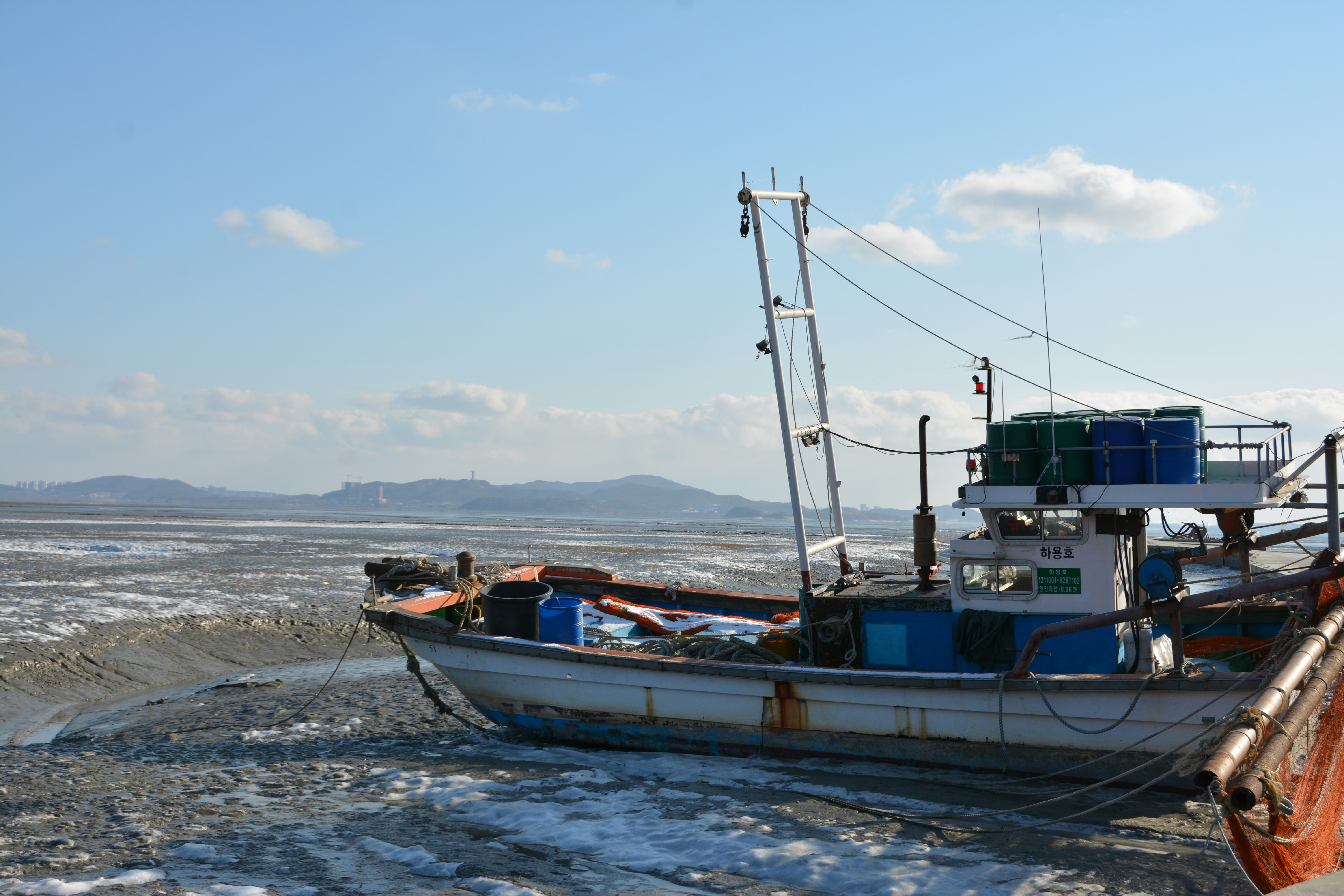 Fishing boat anchored in shallow waters, surrounded by a vast landscape of mudflats and distant hills. 
