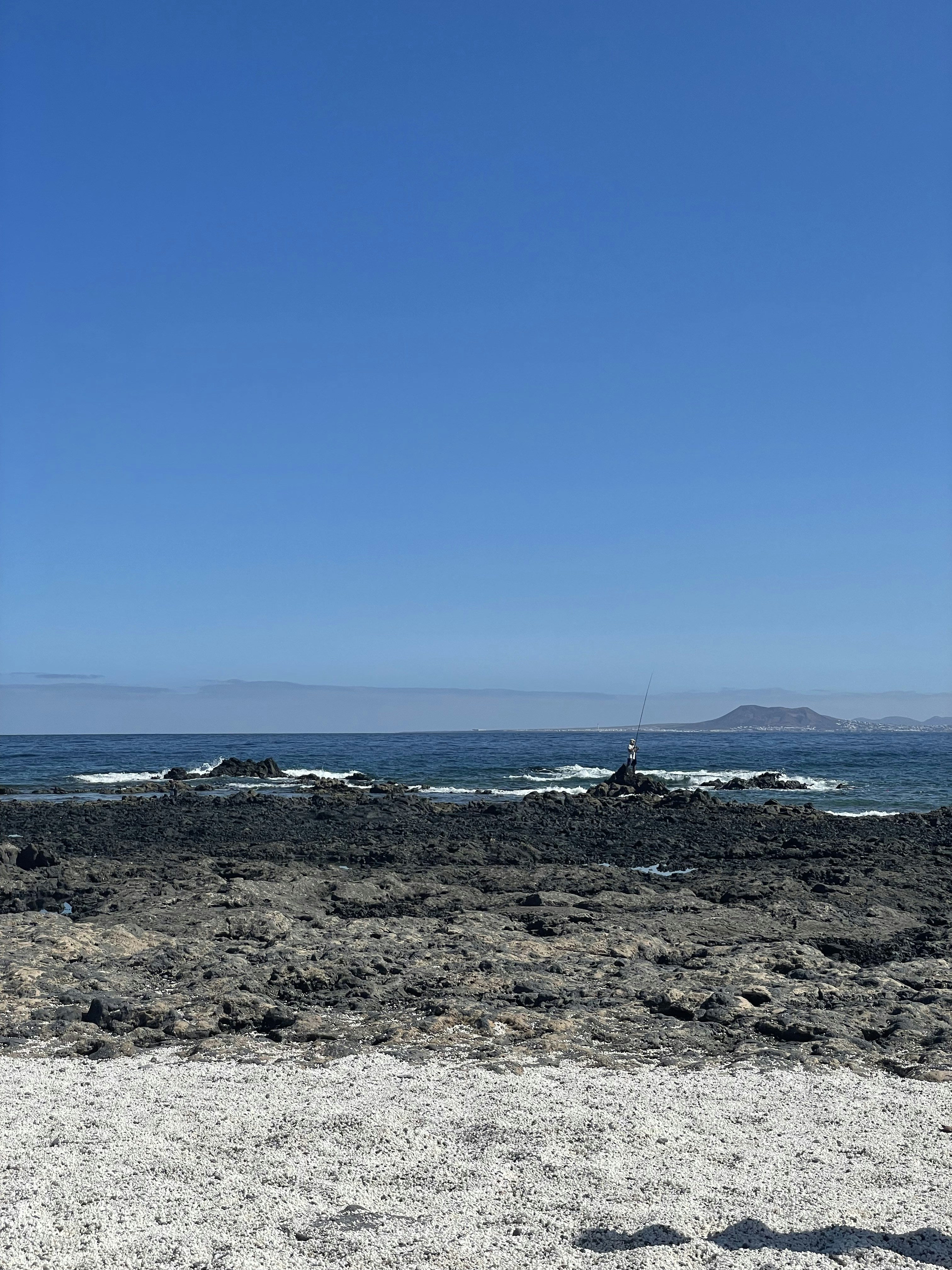 Line of rocks and distant silhouette at a sunlit coastline