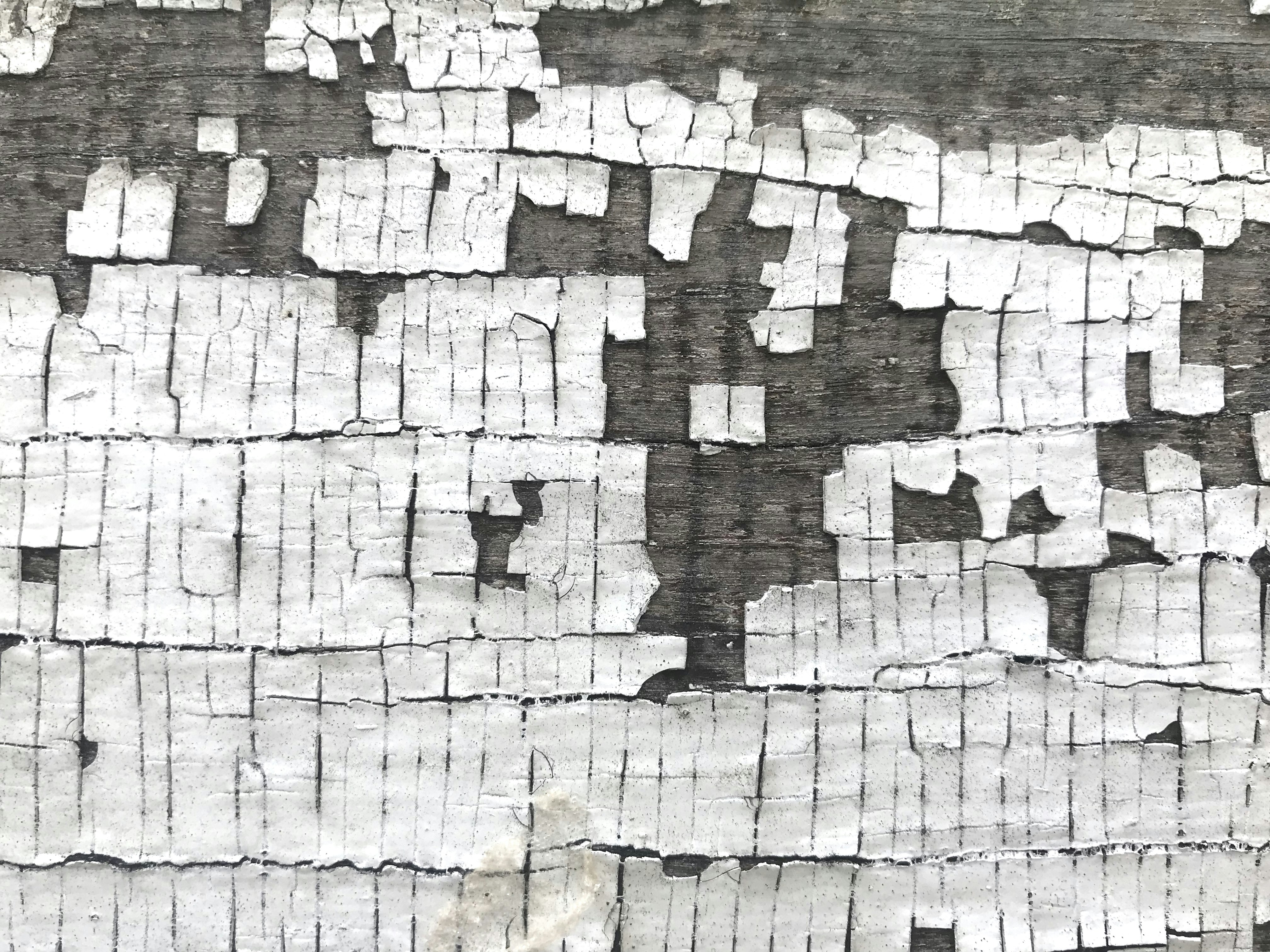 Close-up of peeling white paint on aged wood, revealing the texture and layers beneath.