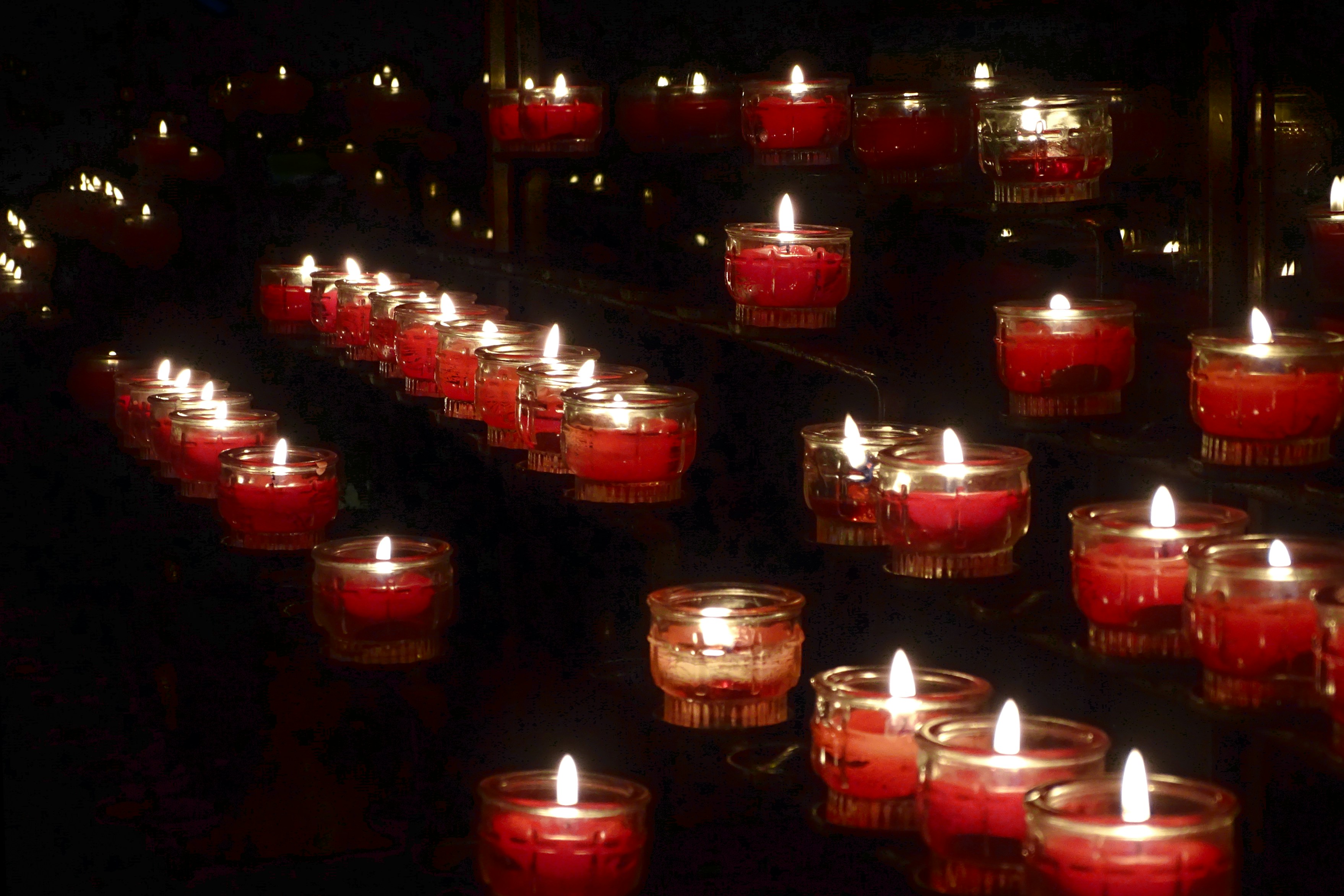 Rows of red candles flicker softly against a dark backdrop, creating a serene and contemplative atmosphere.