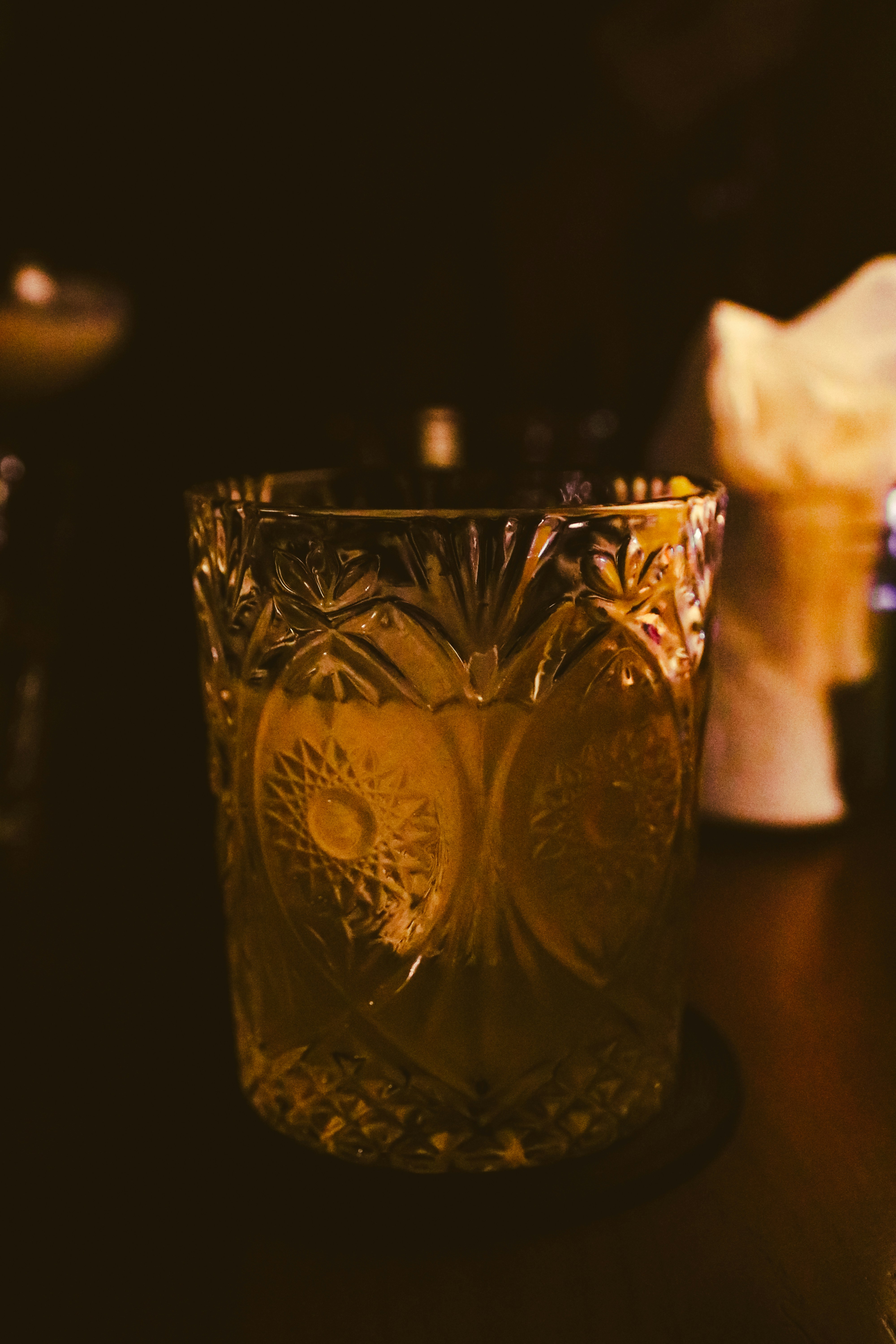 Intricately designed crystal glass filled with a golden beverage, set against a dimly lit background. The play of light accentuates the glass's details.