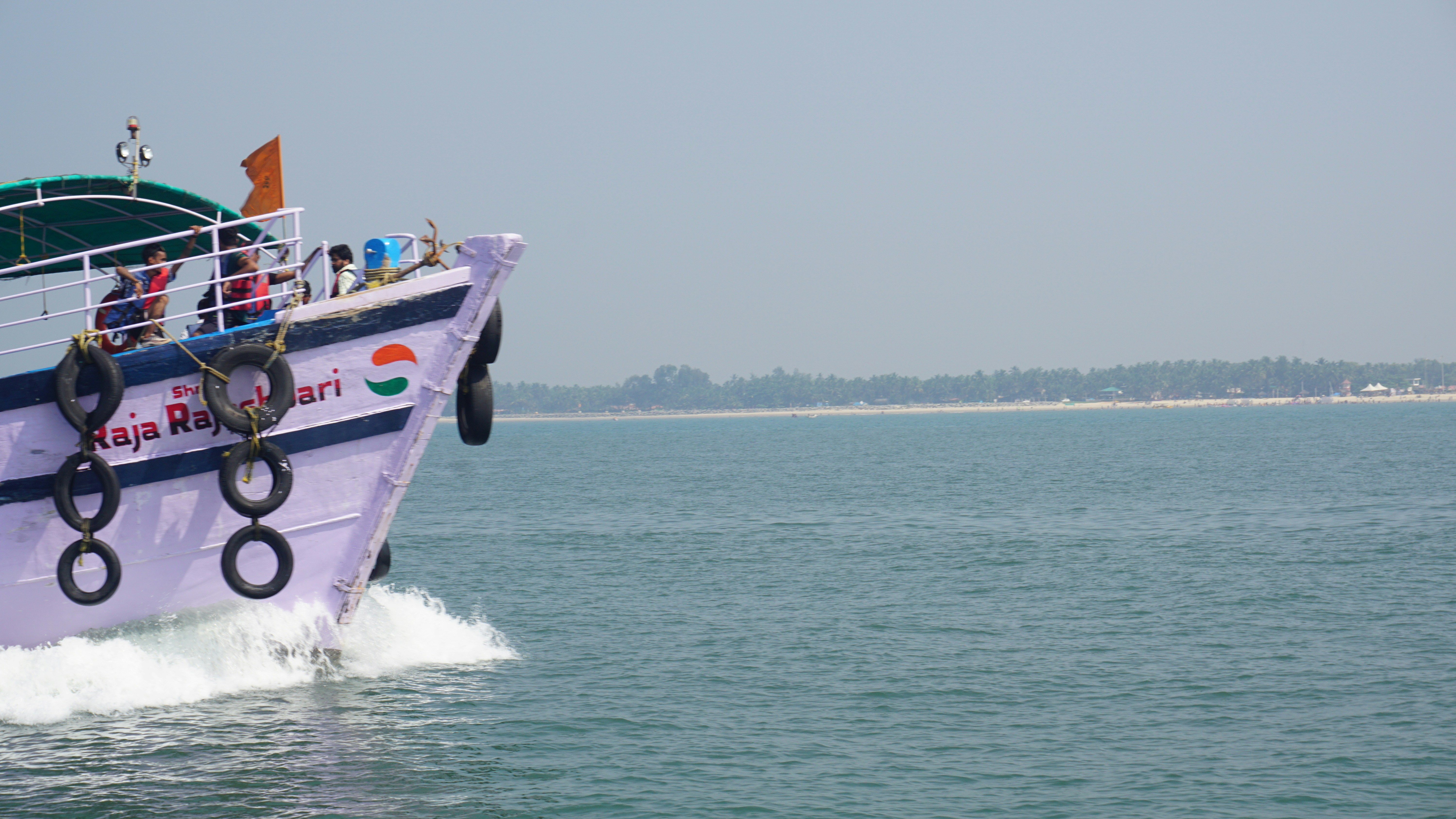 A vibrant boat named Raja Rajdhari cuts through the serene waters, showcasing its colorful bow and passengers enjoying the ride.