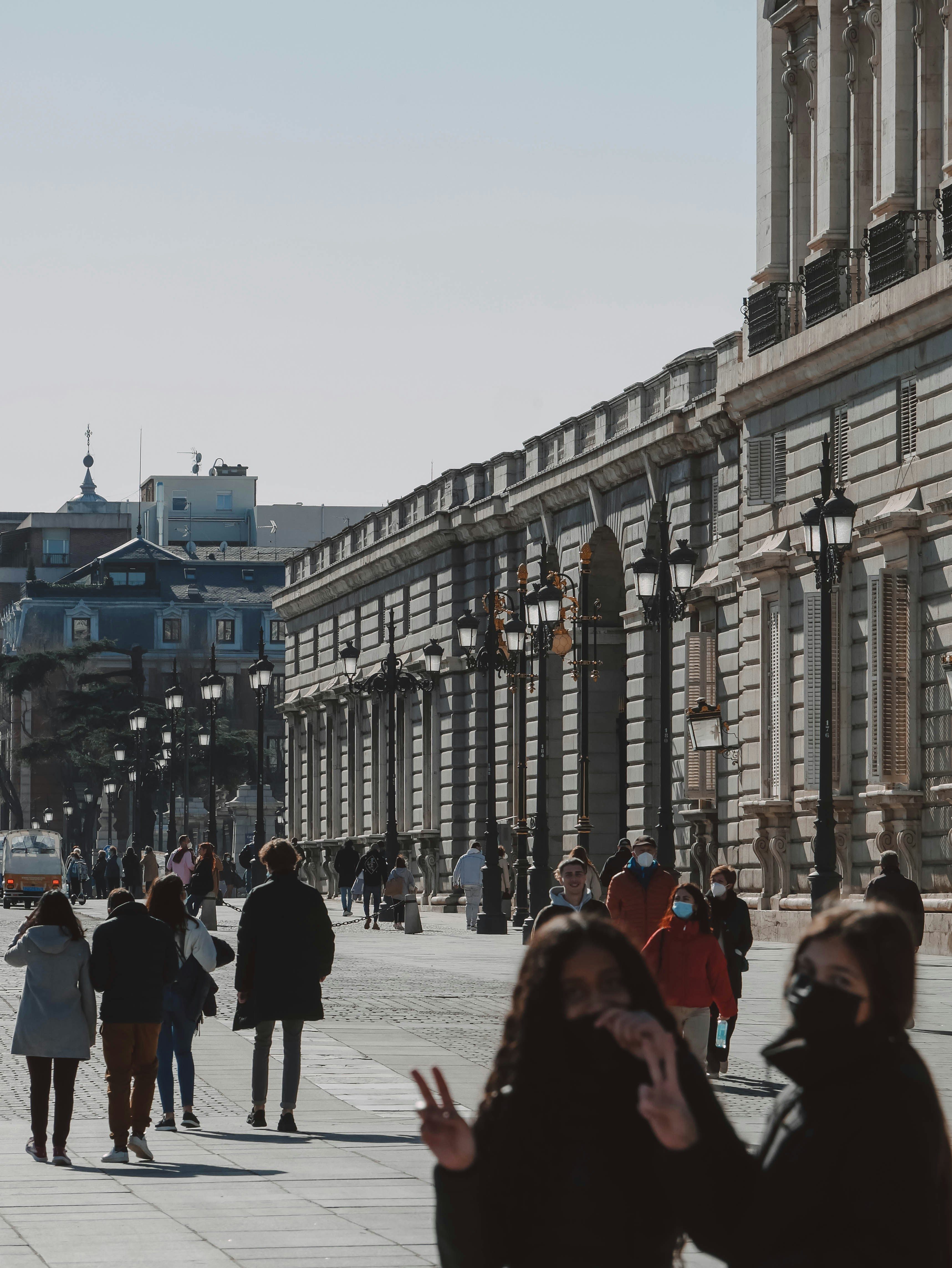 People walking along a sunlit street lined with historic buildings and ornate street lamps.