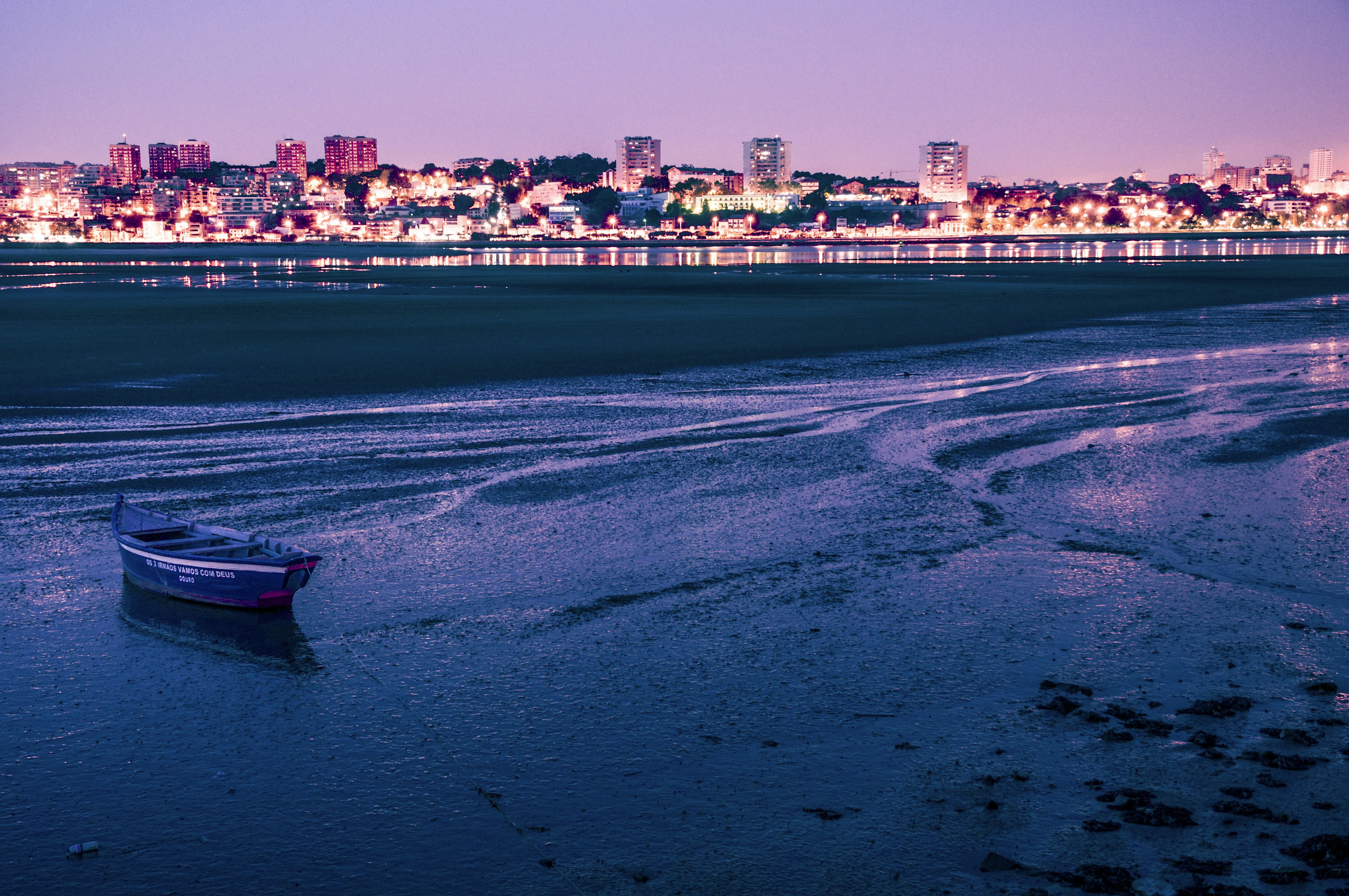 Lone Boat on Indigo Tide Beneath a Neon City Horizon