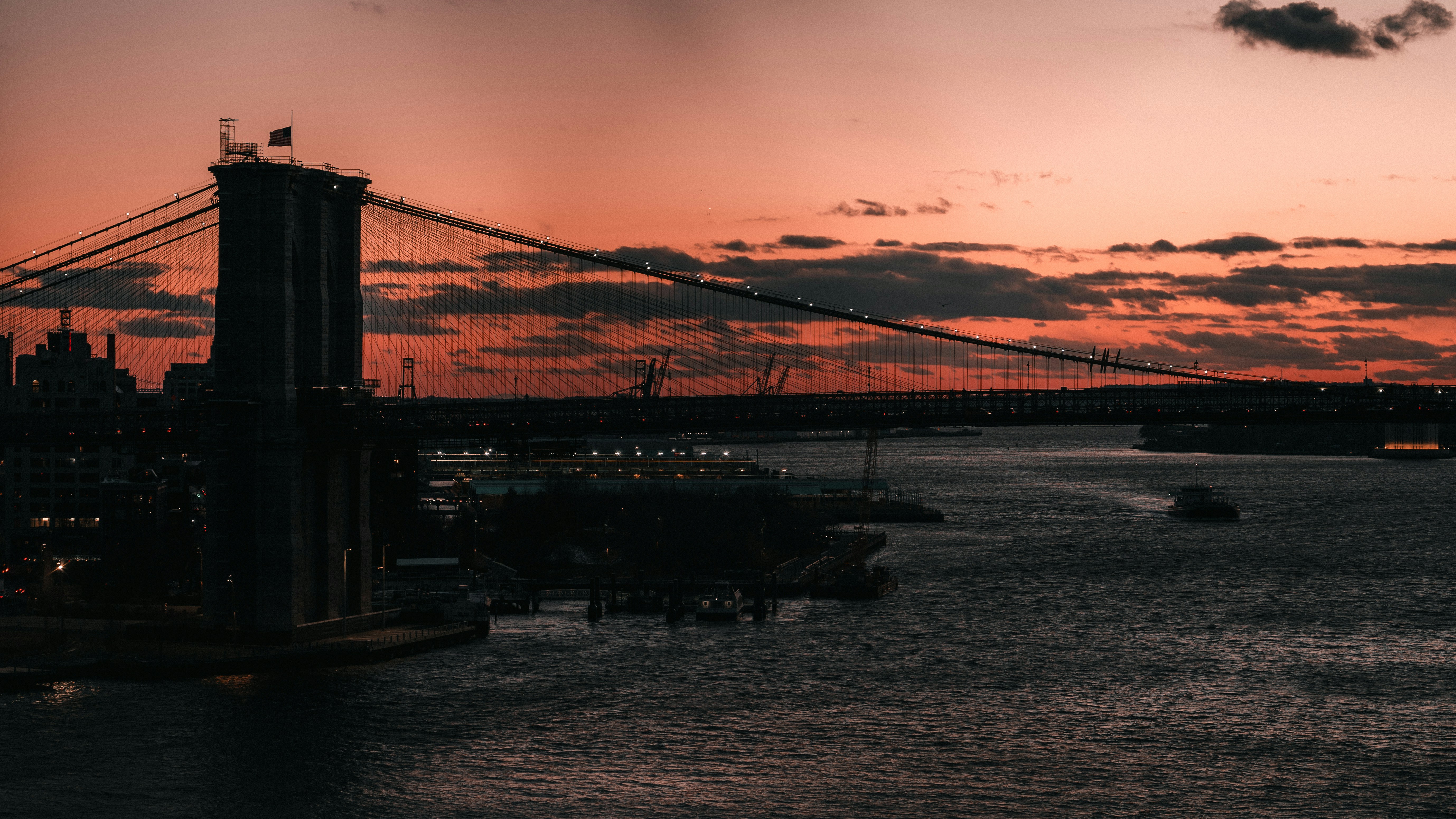 Bridge framed against a vibrant sunset sky with silhouetted cityscape and calm waters.
