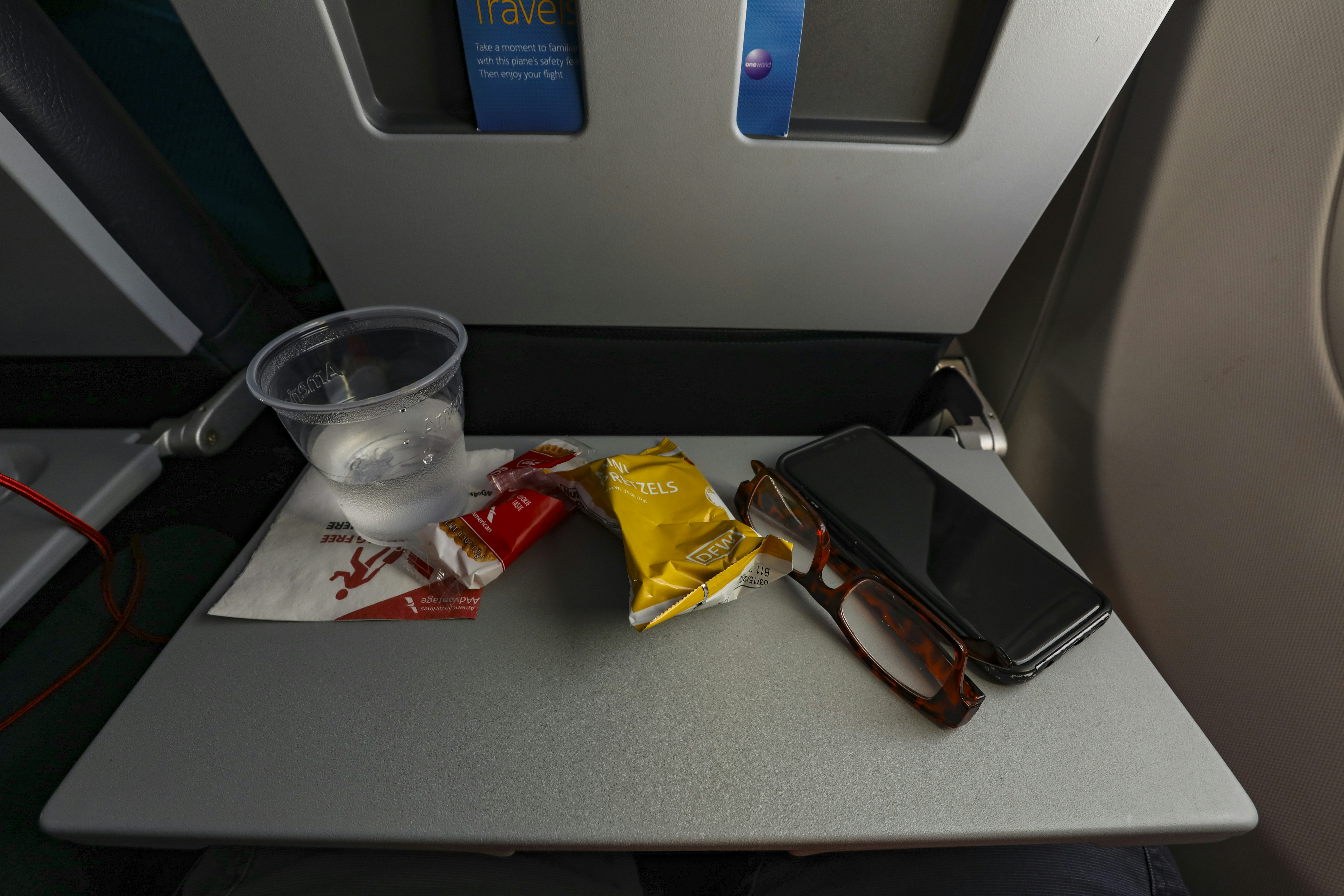 A traveler's snack setup on an airplane tray, featuring a cup of water, assorted snacks, and a smartphone. The scene captures the essence of in-flight convenience.