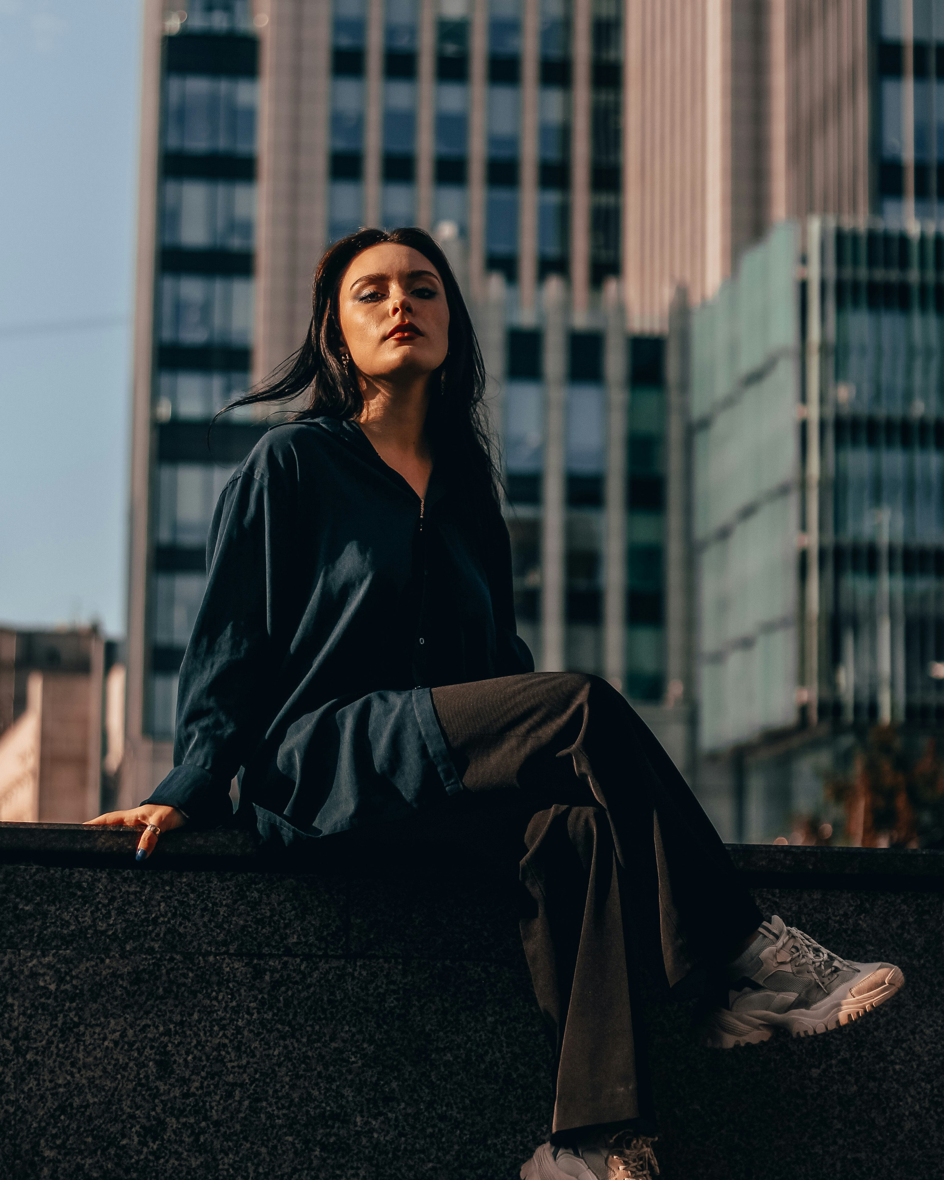 A woman sitting on a ledge in front of tall buildings photo – Free Girl ...