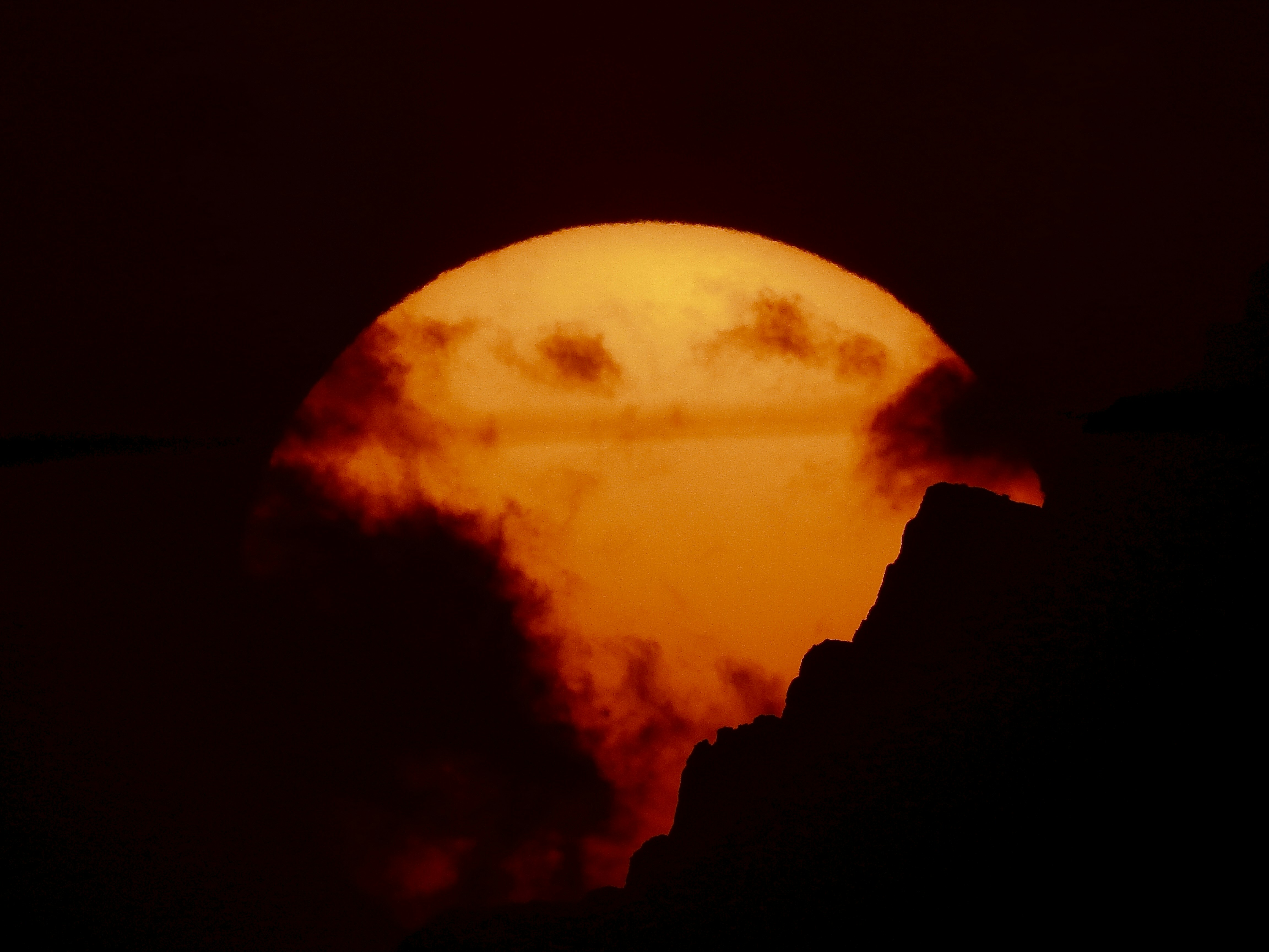 the sun is setting over a mountain with clouds