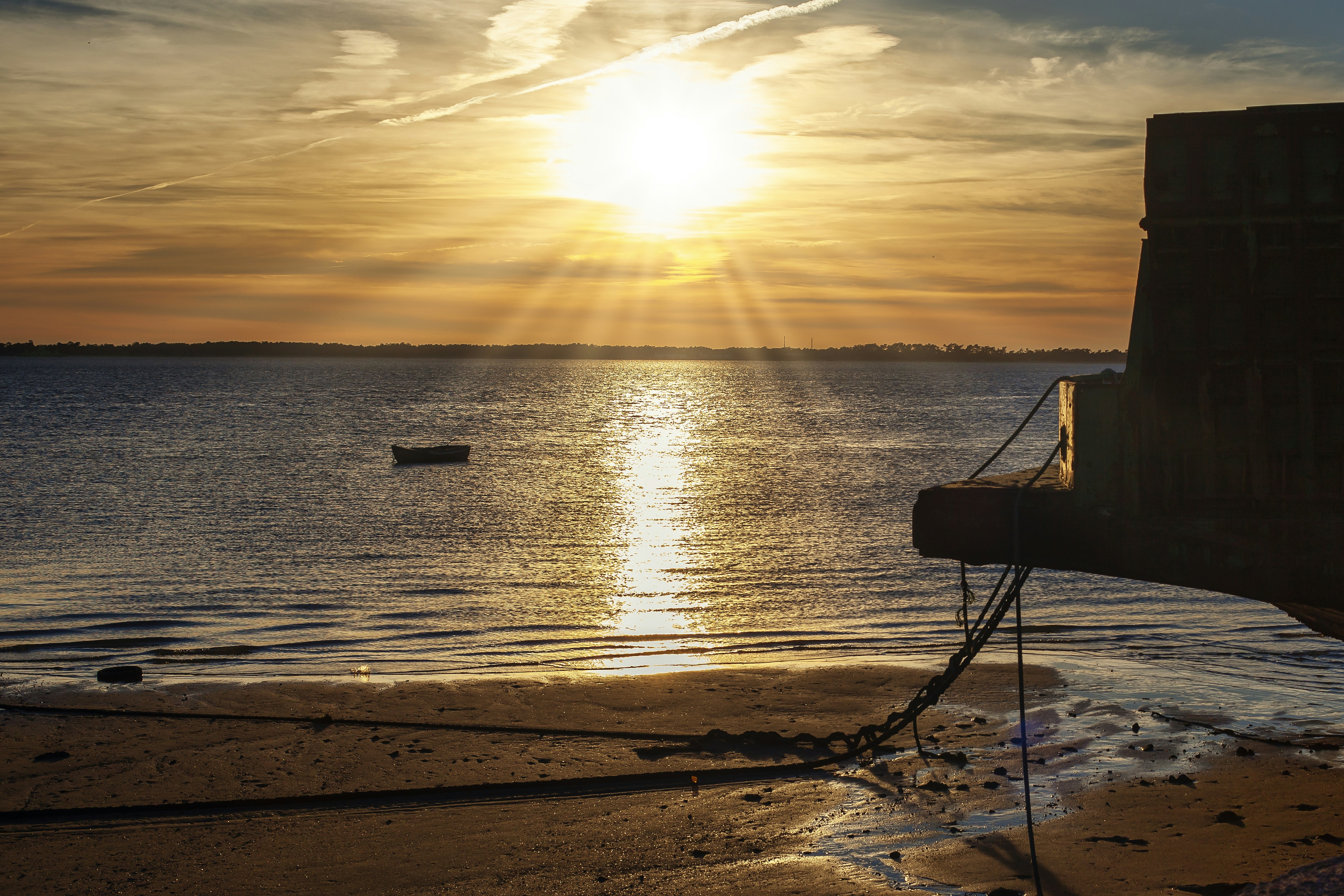 Golden sunset casting reflections on a calm sea with a lone boat in the distance.