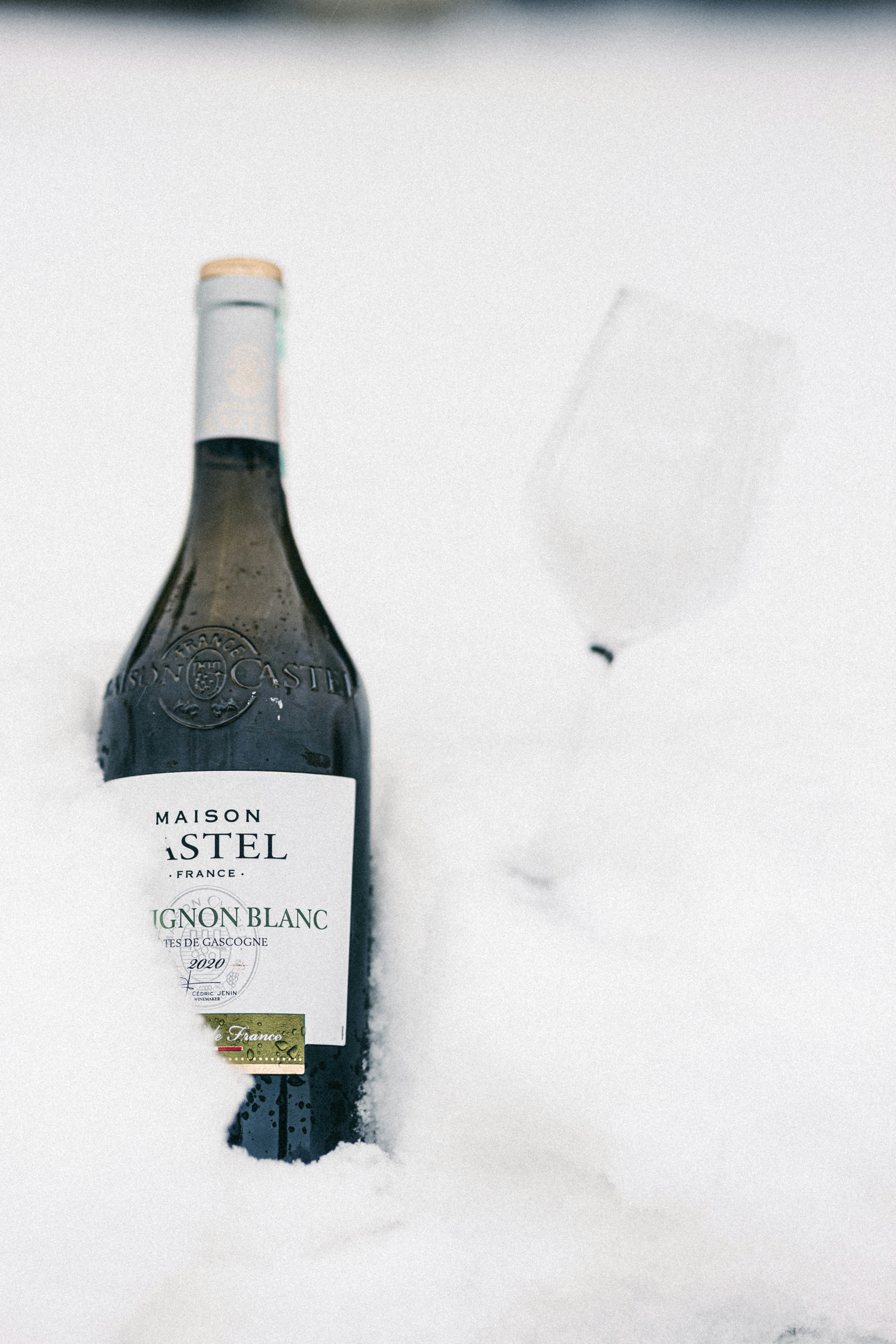 A bottle of Maison Castel Sauvignon Blanc partially buried in snow beside a frosted wine glass, evoking a serene winter ambiance.