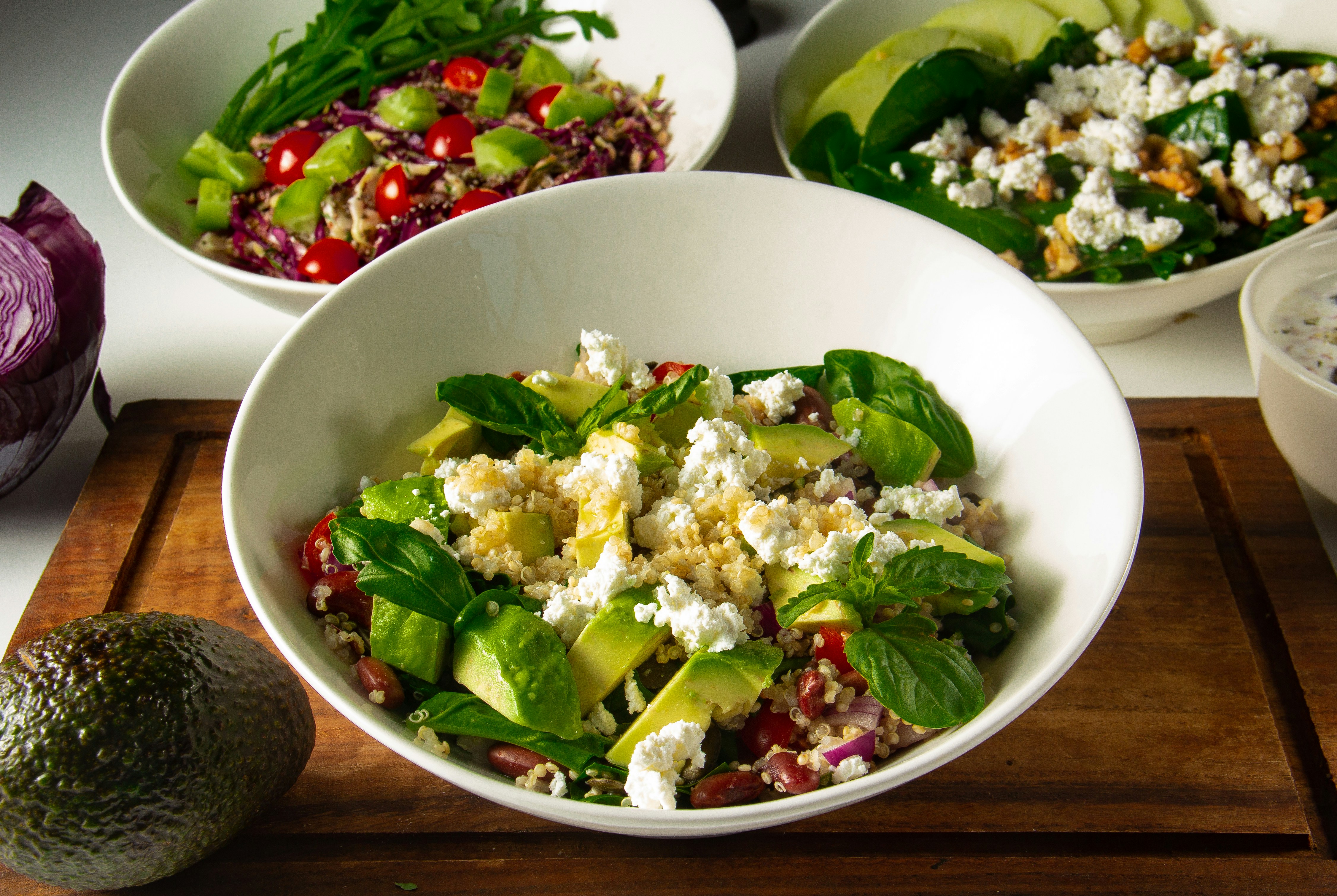 Vibrant salad featuring fresh greens, avocado, and crumbled cheese, surrounded by colorful bowls of additional salads. Perfect for a healthy meal.