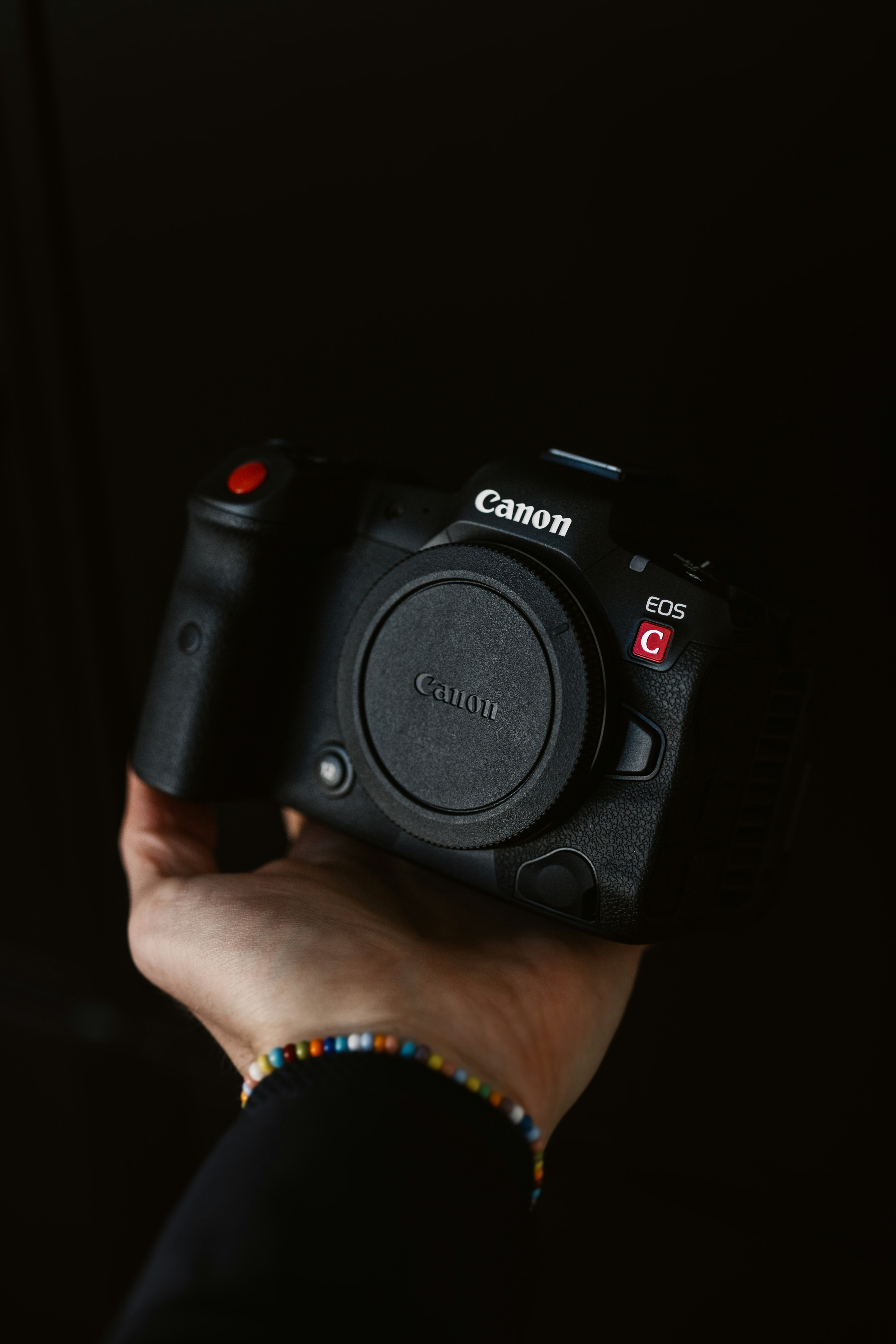 A Canon EOS camera held in a hand against a dark backdrop, showcasing its sleek design and functionality.