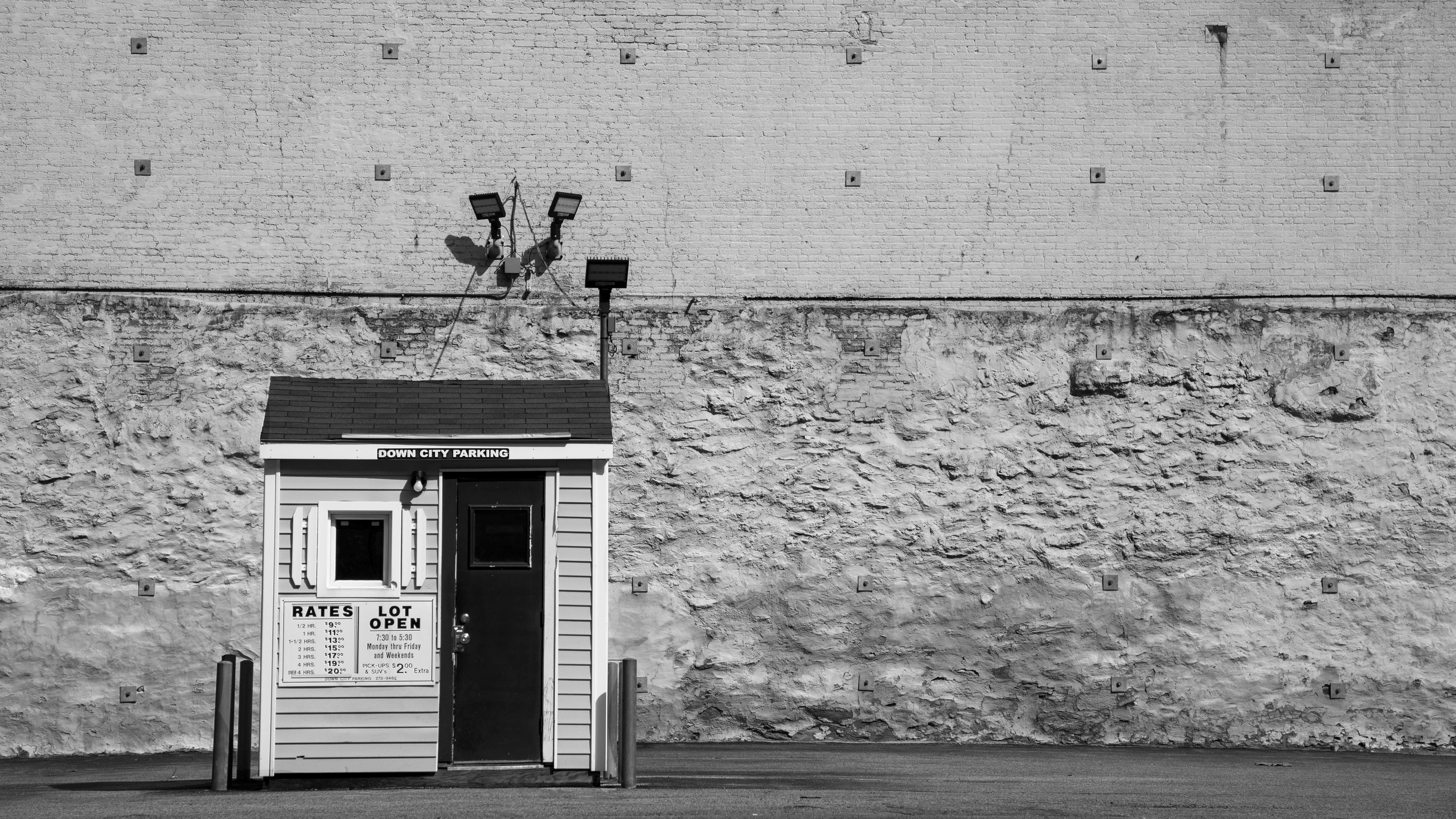A solitary parking booth stands against a textured wall, embodying a sense of forgotten urban life. The stark black and white tones enhance the mood of desolation.