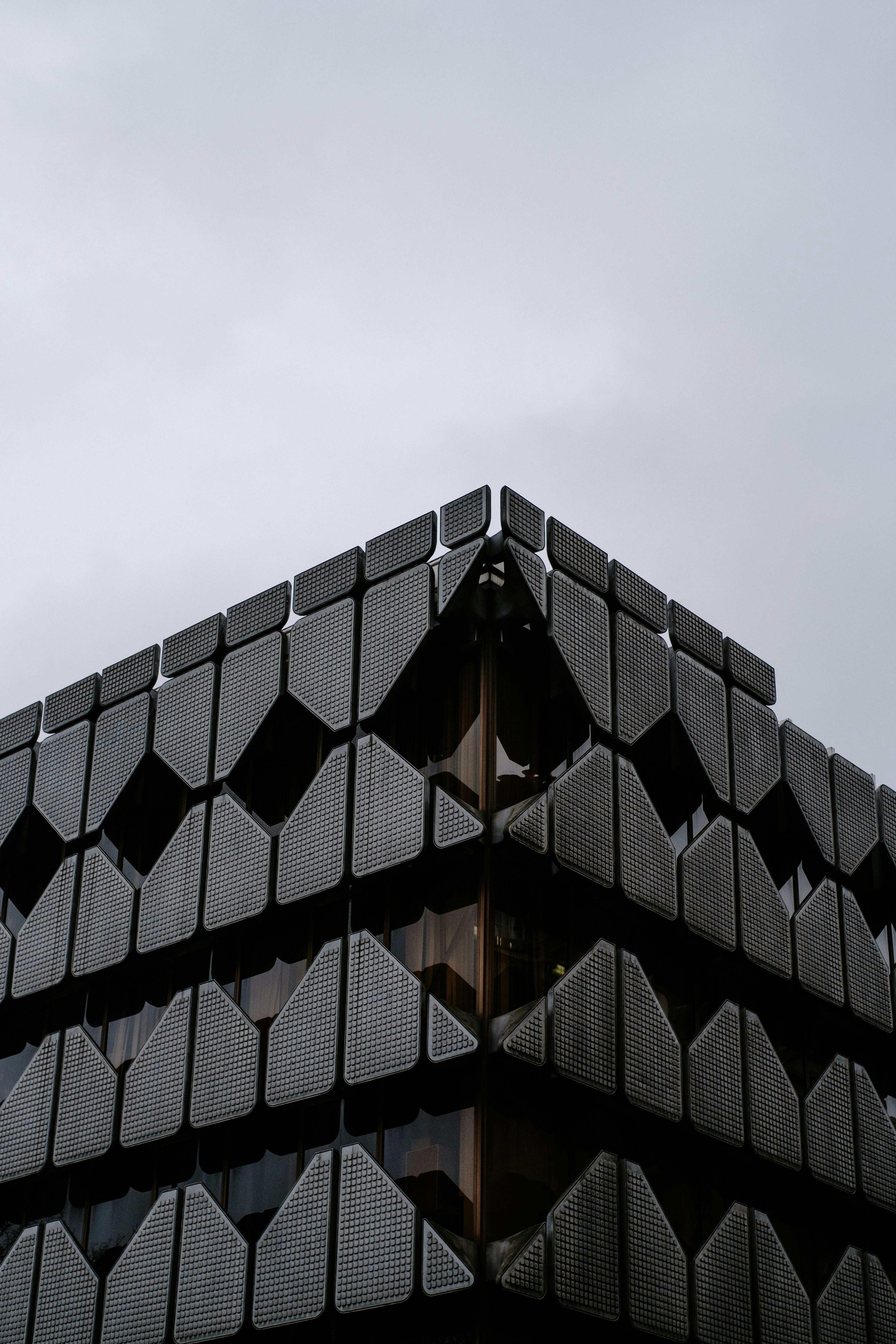Angular facade of a contemporary building reflecting light against a cloudy sky.