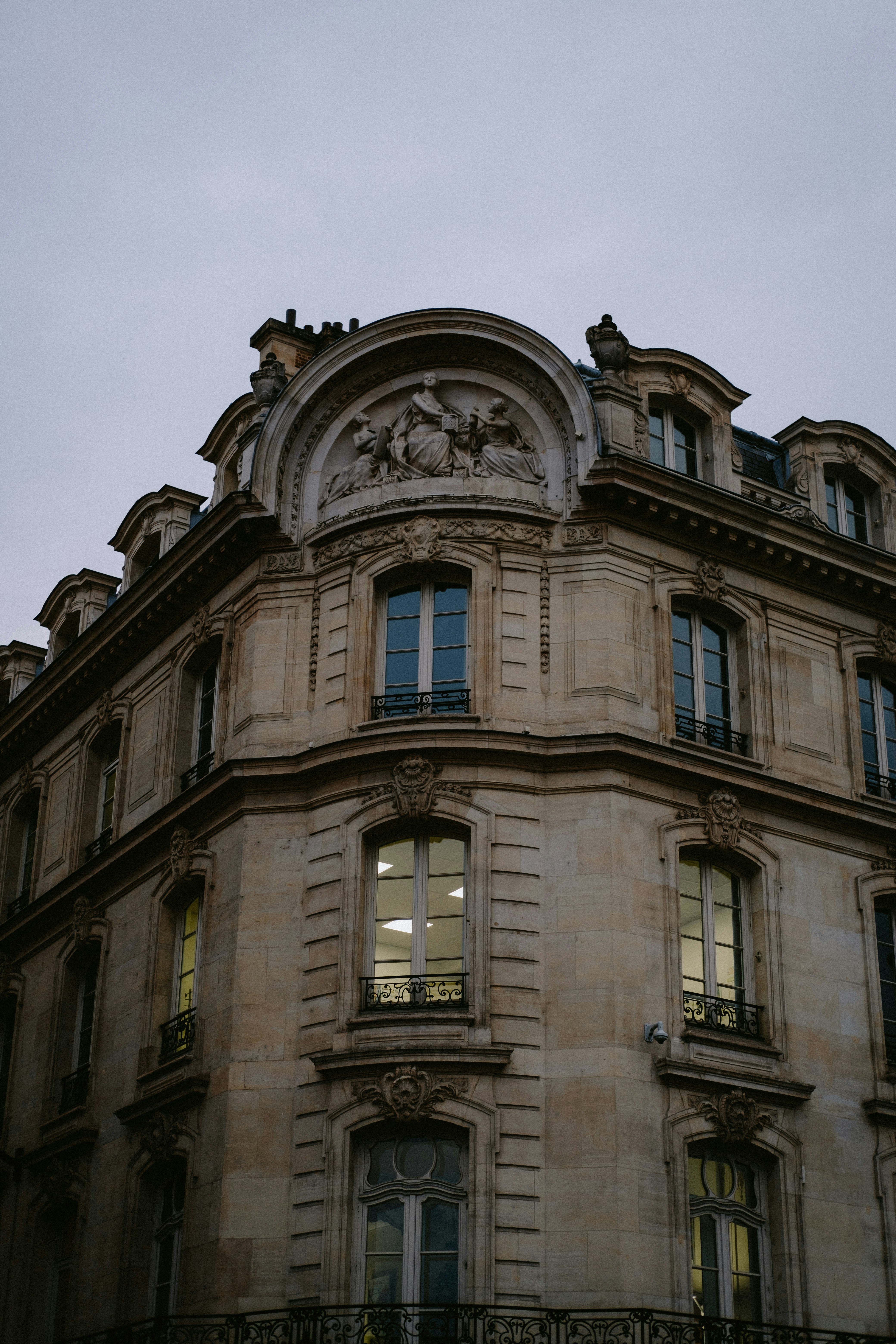 Ornate architectural features on a historic building, showcasing intricate carvings and large windows. The soft evening light enhances the facade's textures.
