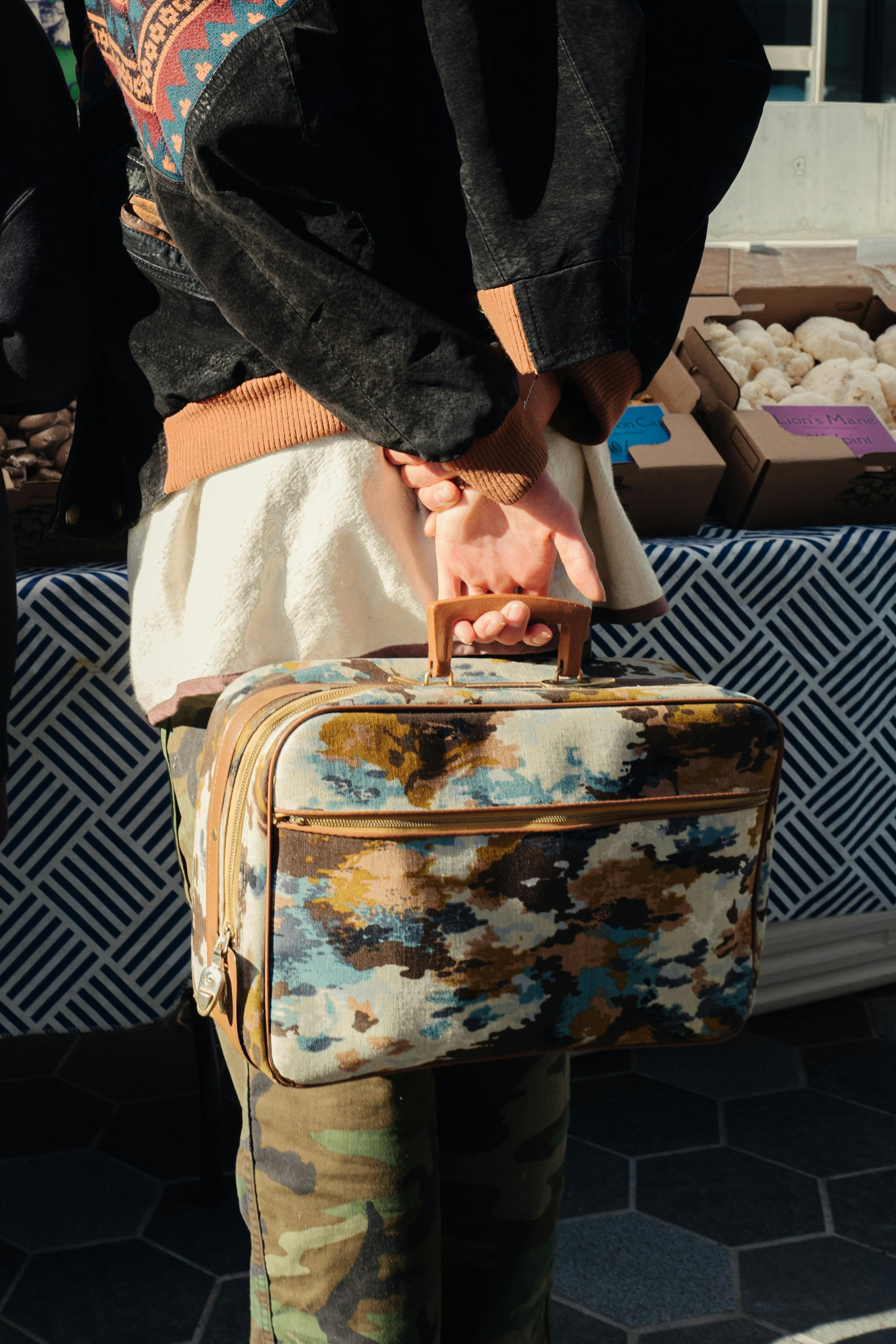 Person holding a patterned bag, showcasing a blend of colors and textures, against a backdrop of market items.