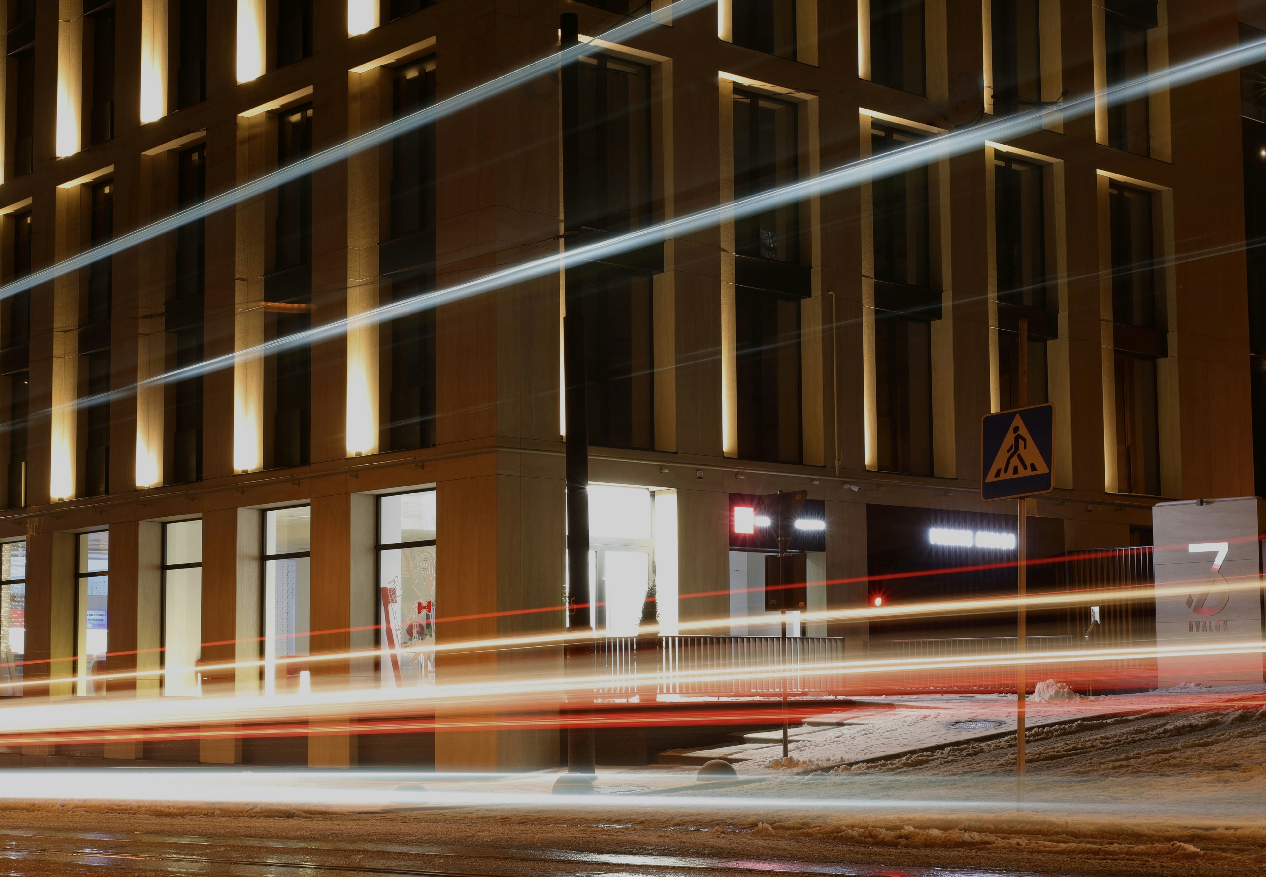 Dynamic light trails streak past a modern building with illuminated windows at night. The scene captures urban energy and architectural design.