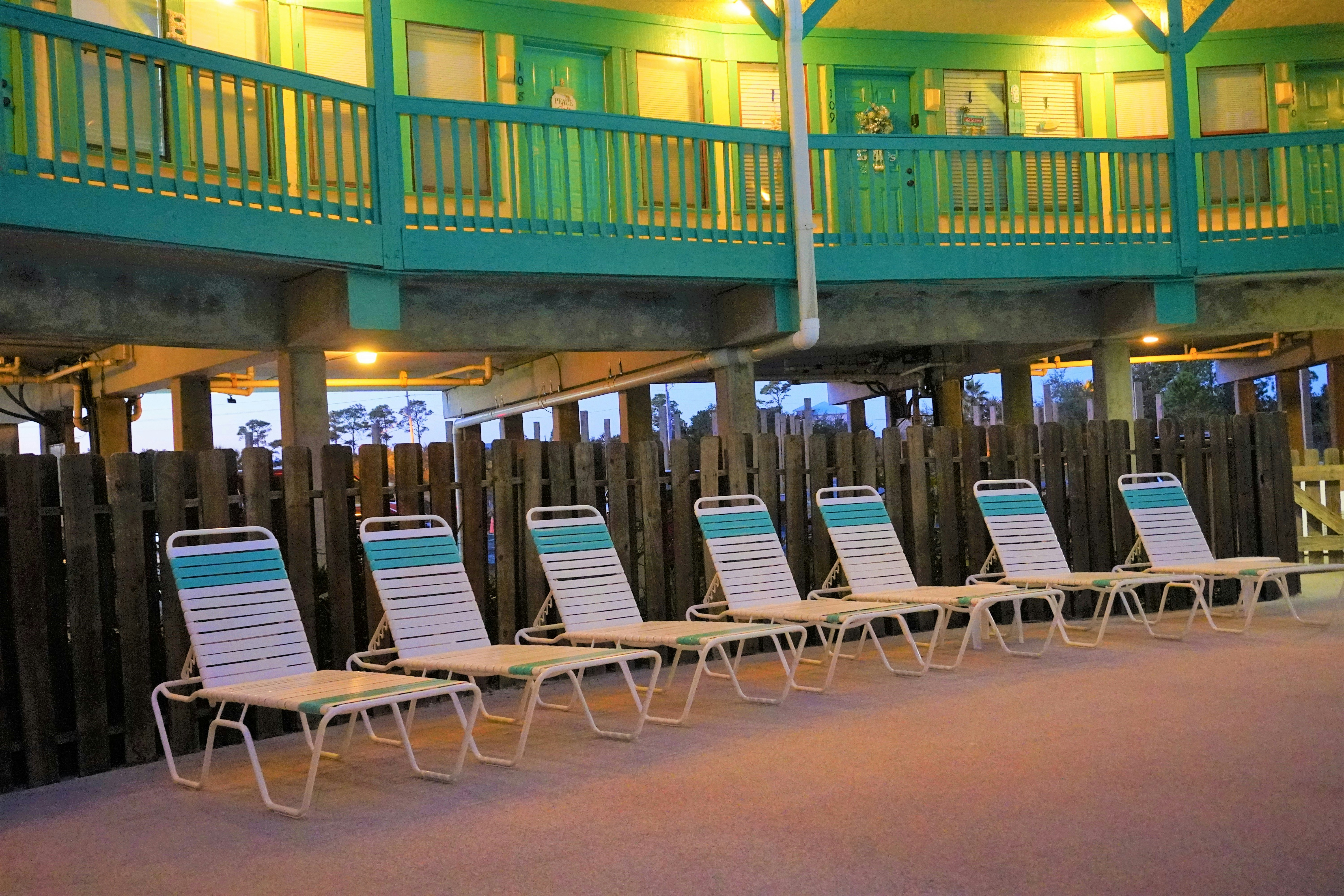 A row of lawn chairs lined up under a teal-lit building at twilight.