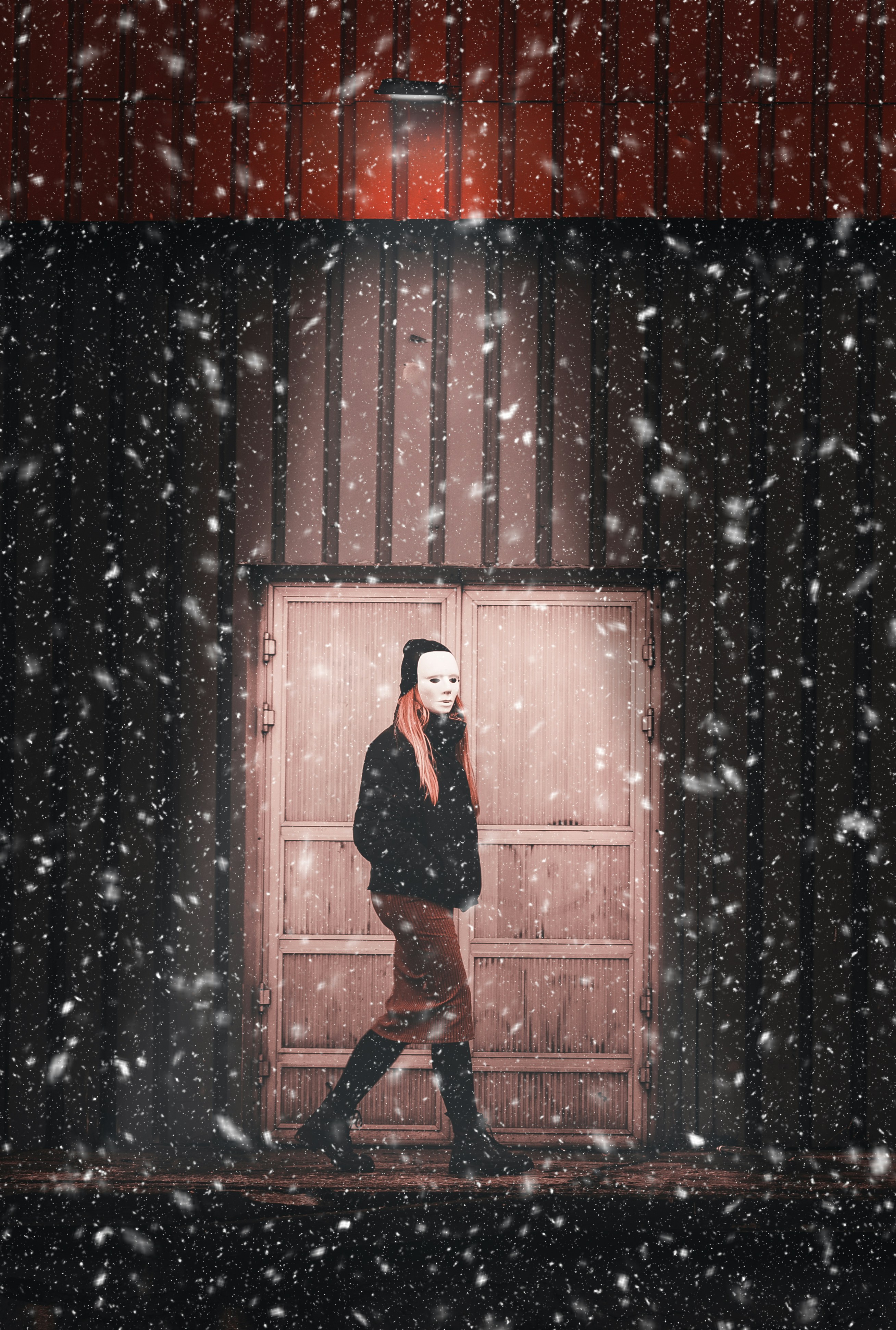 A figure walks through falling snow in front of a rustic door, evoking a sense of solitude and tranquility. The scene captures the essence of winter's quiet beauty.