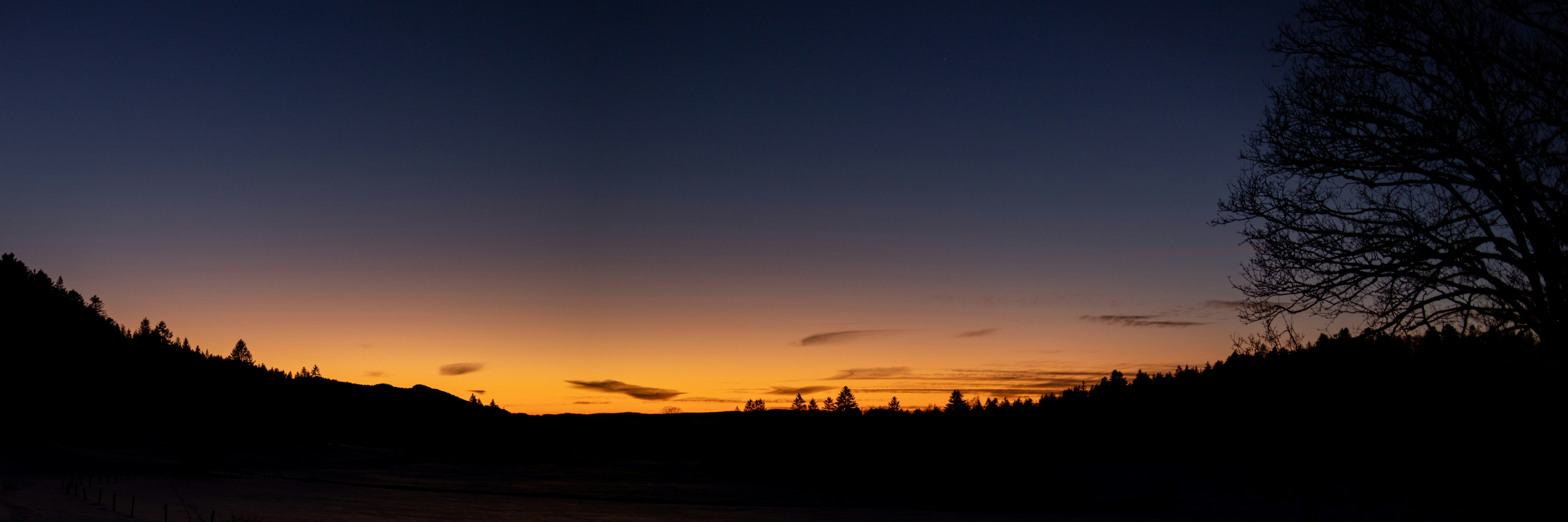 Sunset casting a warm glow over silhouetted mountains and trees.