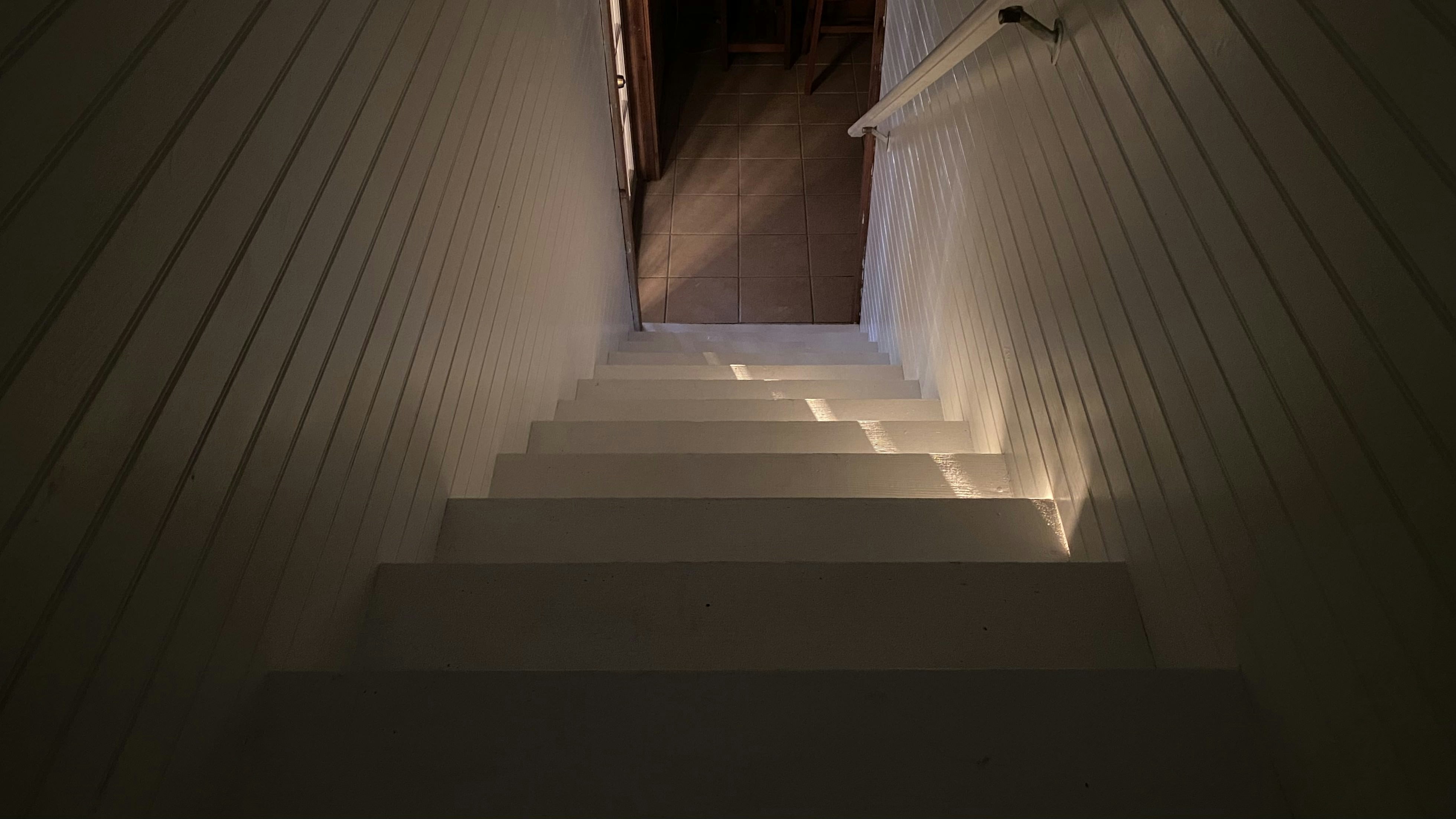 Sunlight streaming down a staircase, illuminating the white steps leading to a wooden floor at the bottom. The scene evokes a sense of warmth and invitation.