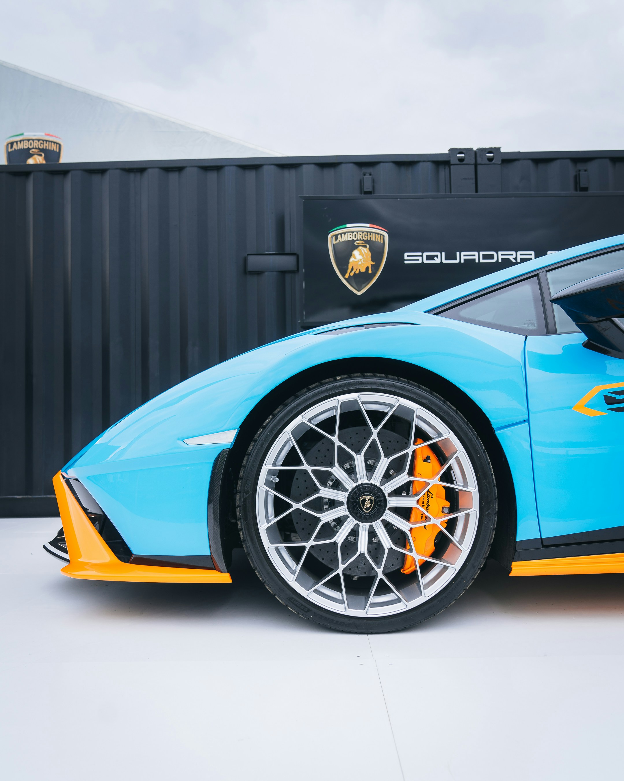 A striking side view of a Lamborghini featuring a vibrant aqua color and intricate wheel design against a contrasting background.