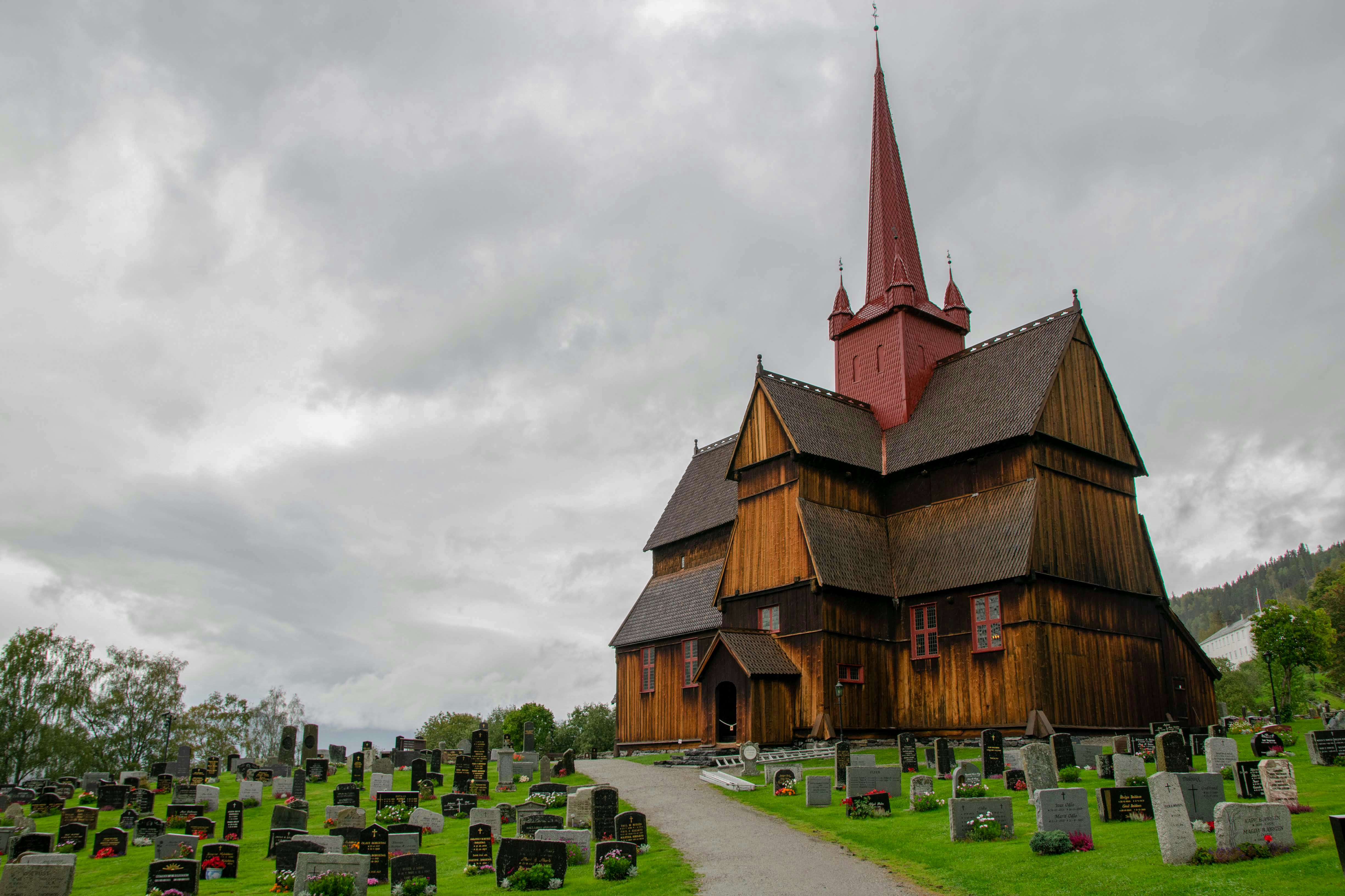 Historic wooden church surrounded by gravestones in a serene graveyard, under an overcast sky.