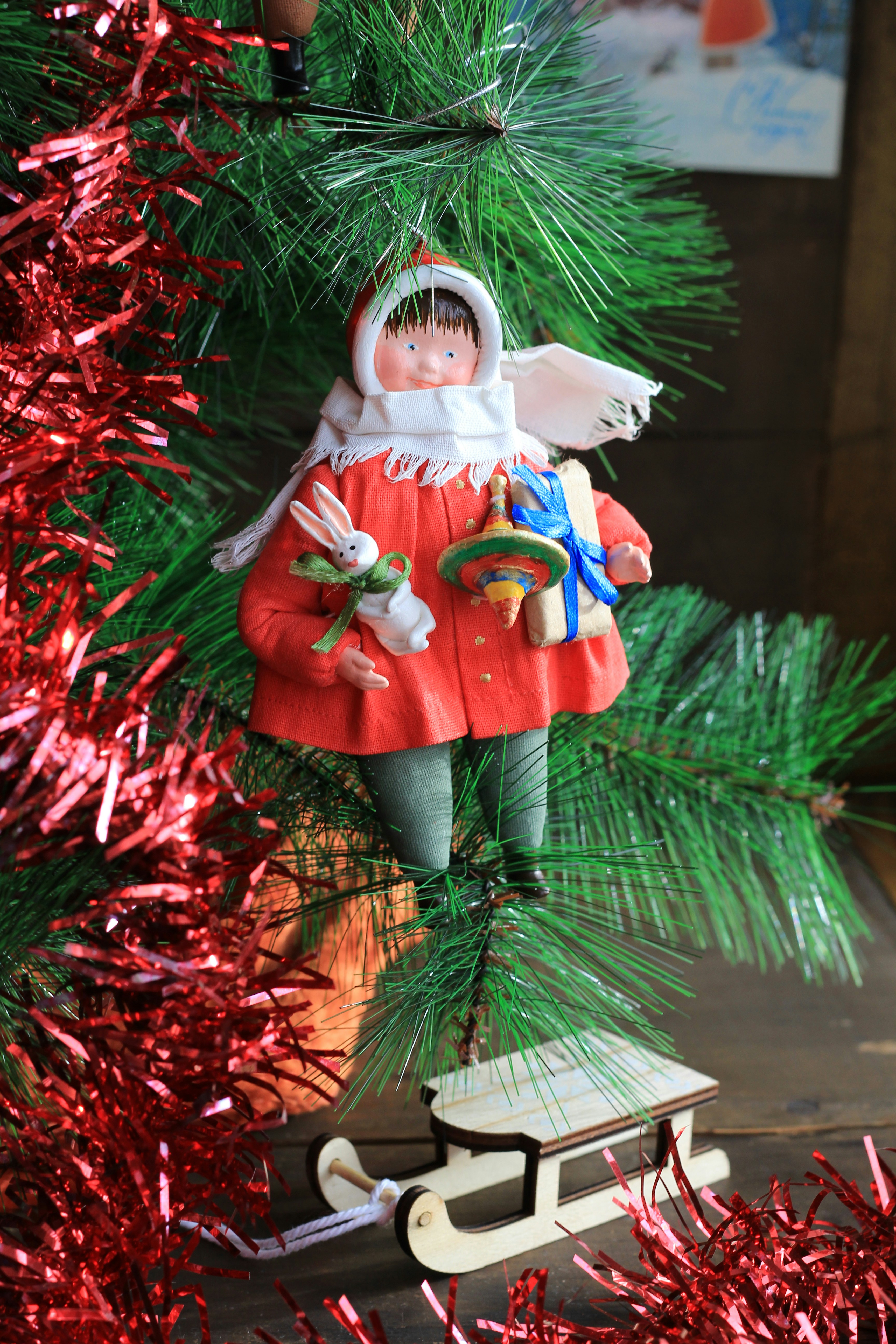 Ornament on a Mini Sleigh: A Festive Figure Under Green Pine and Red Tinsel