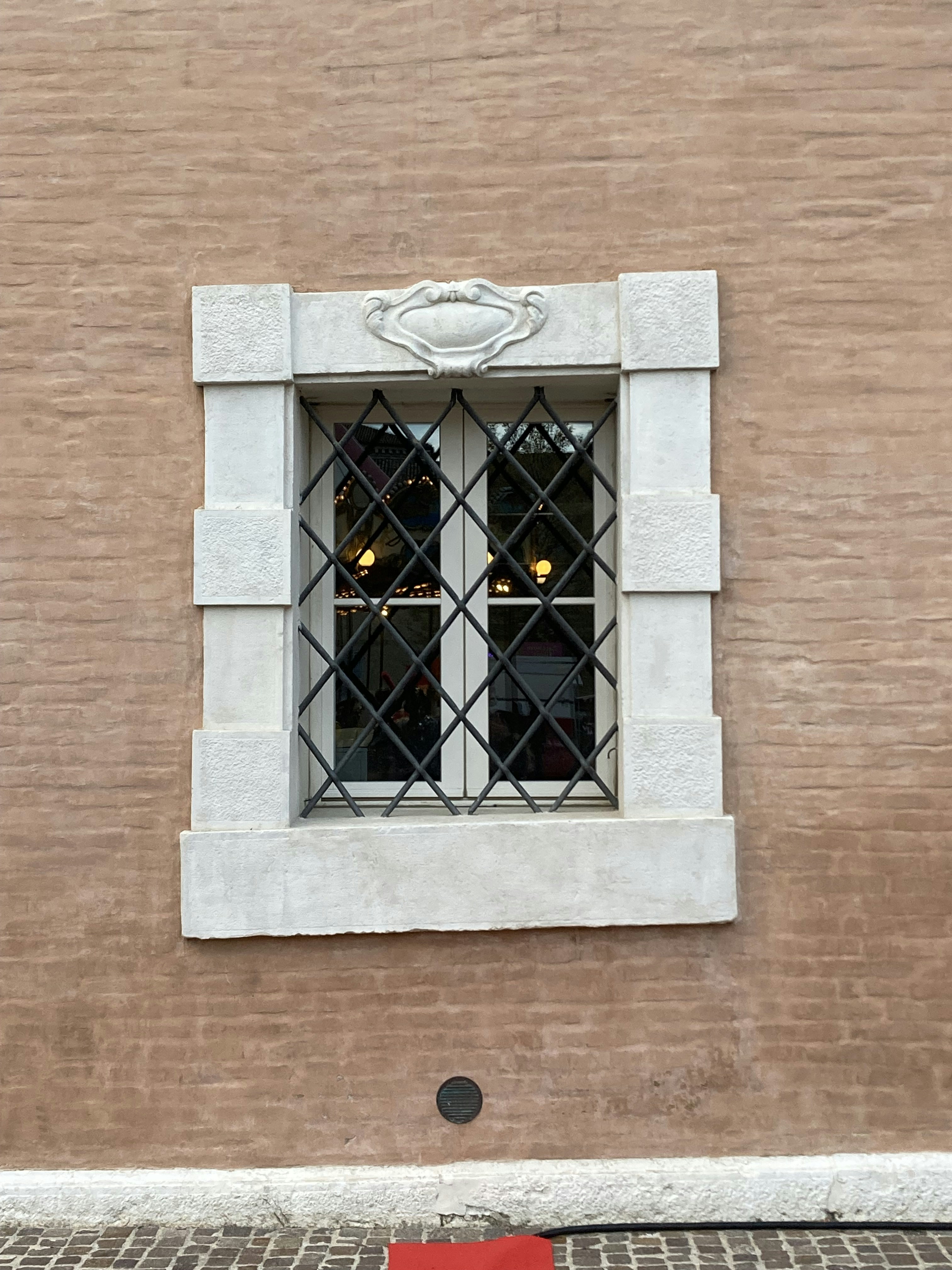 A decorative window framed by textured stone, featuring a diamond-patterned grille and a carved motif above. The warm tones of the wall provide a historical backdrop.