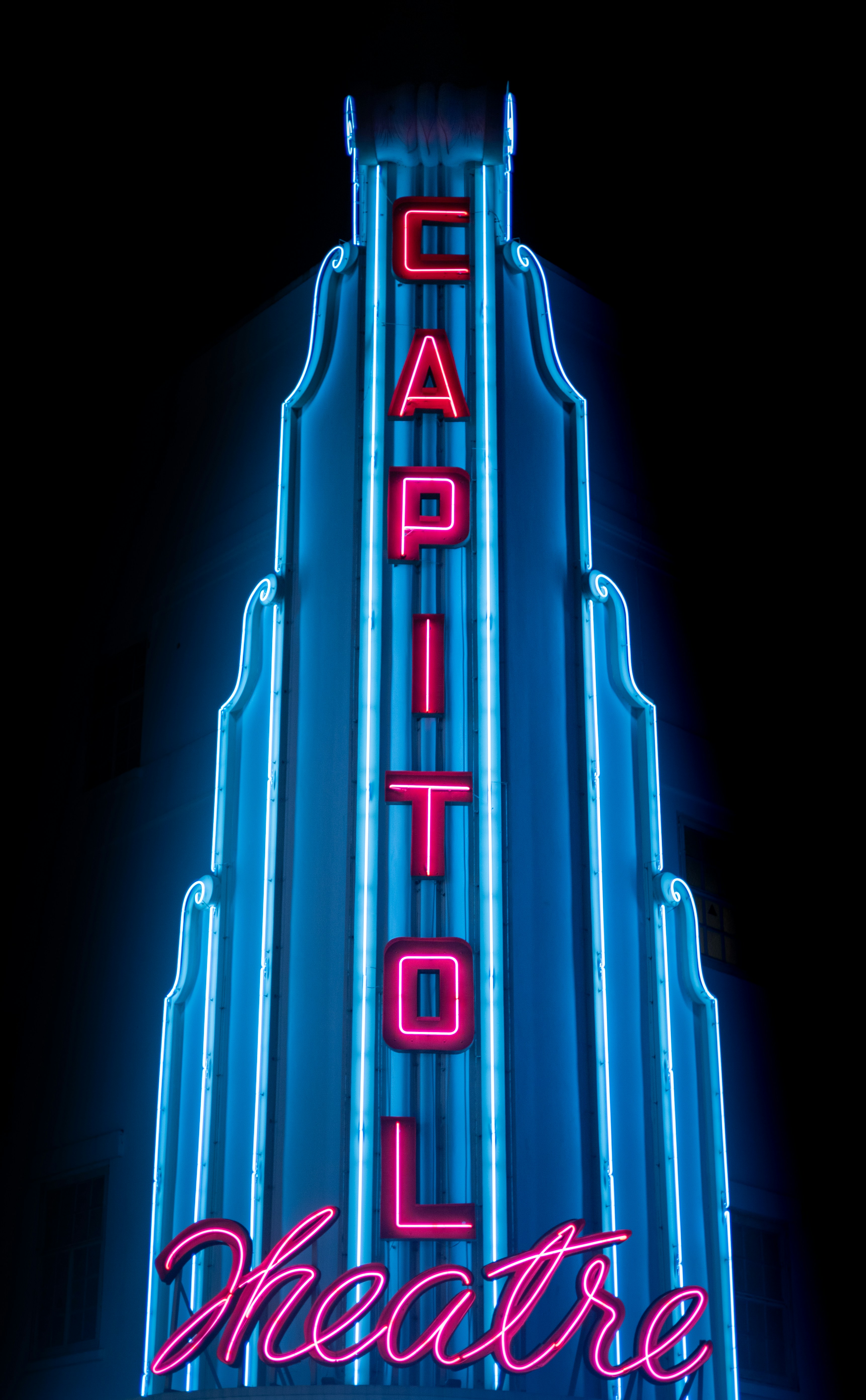 Vibrant neon sign of the Capitol Theatre illuminated against a dark backdrop, showcasing retro typography and striking colors.